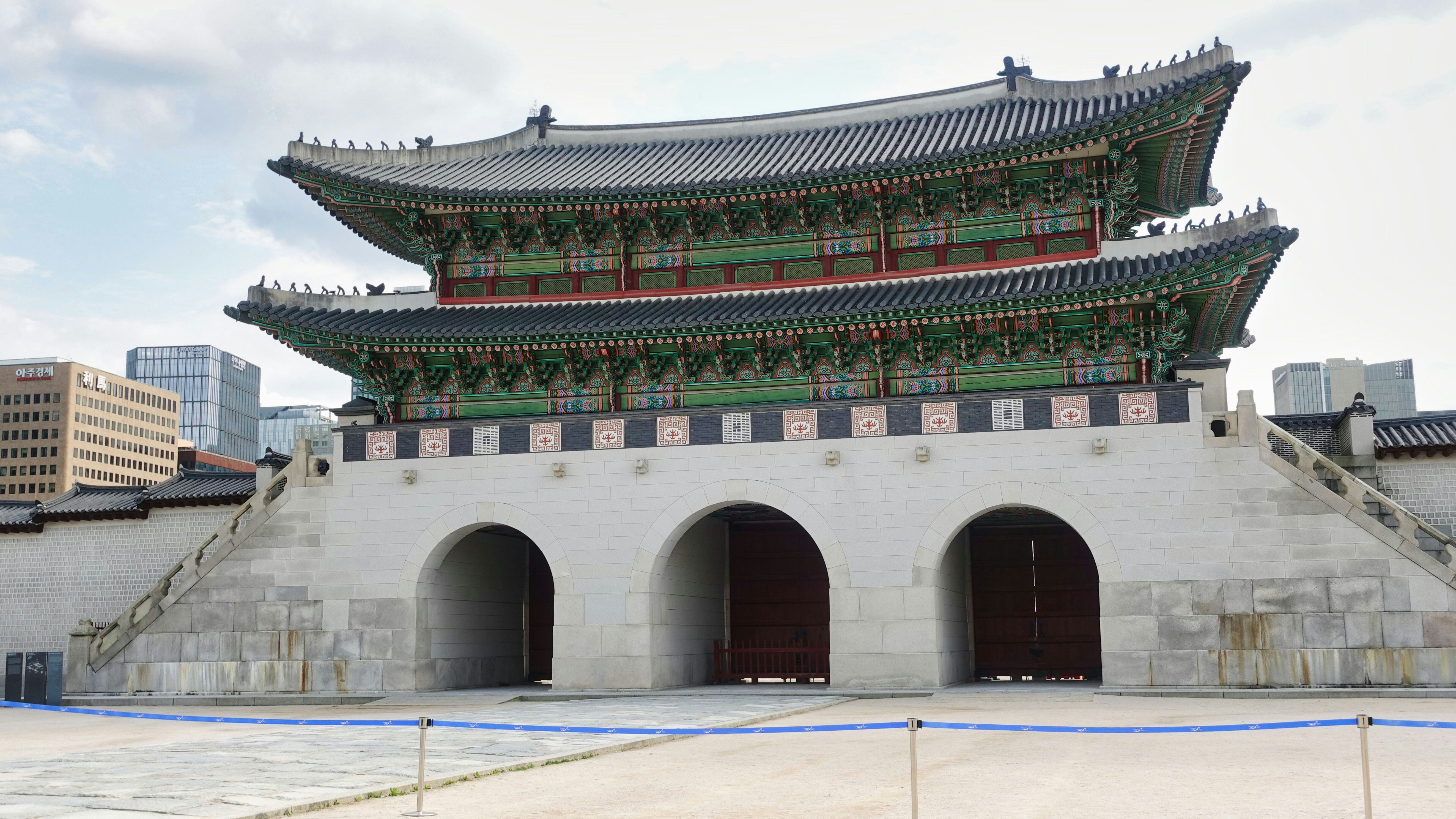 Historic gate with tiered roof and multiple arches surrounded by modern cityscape.