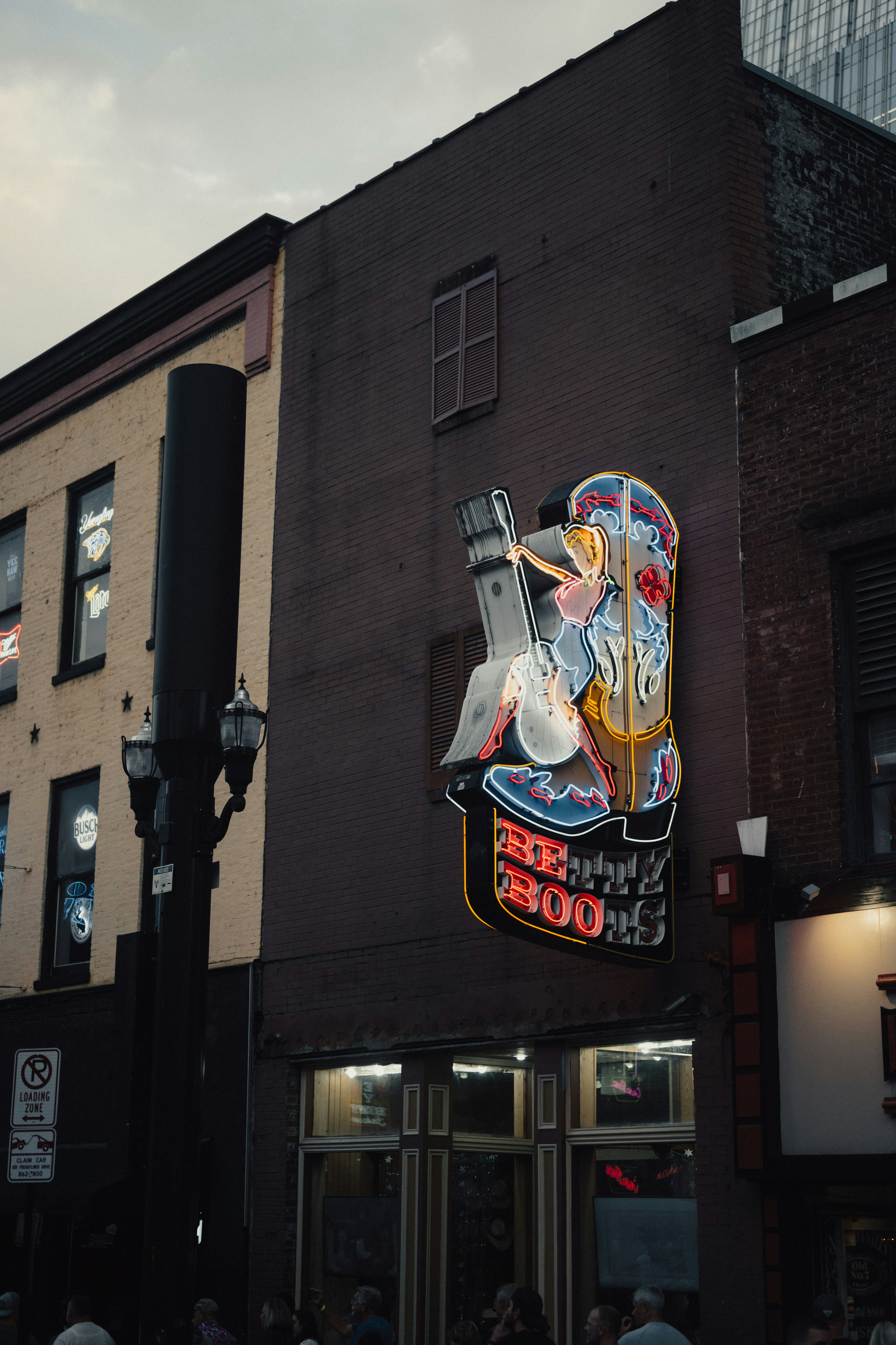Neon Pin-Up on a Guitar Sign Illuminates a Brick Street at Dusk