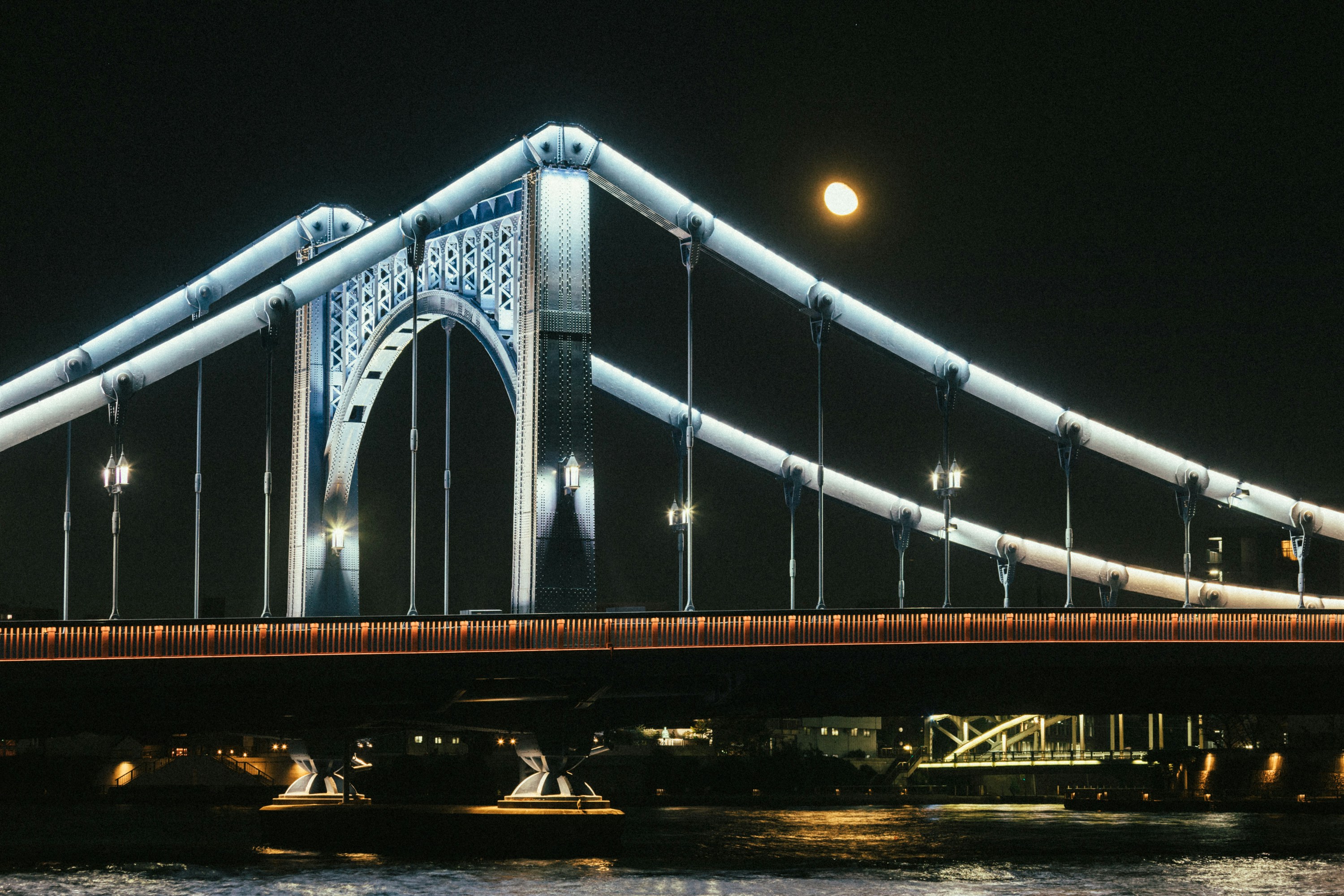 A bridge lit up at night with a full moon in the background photo ...