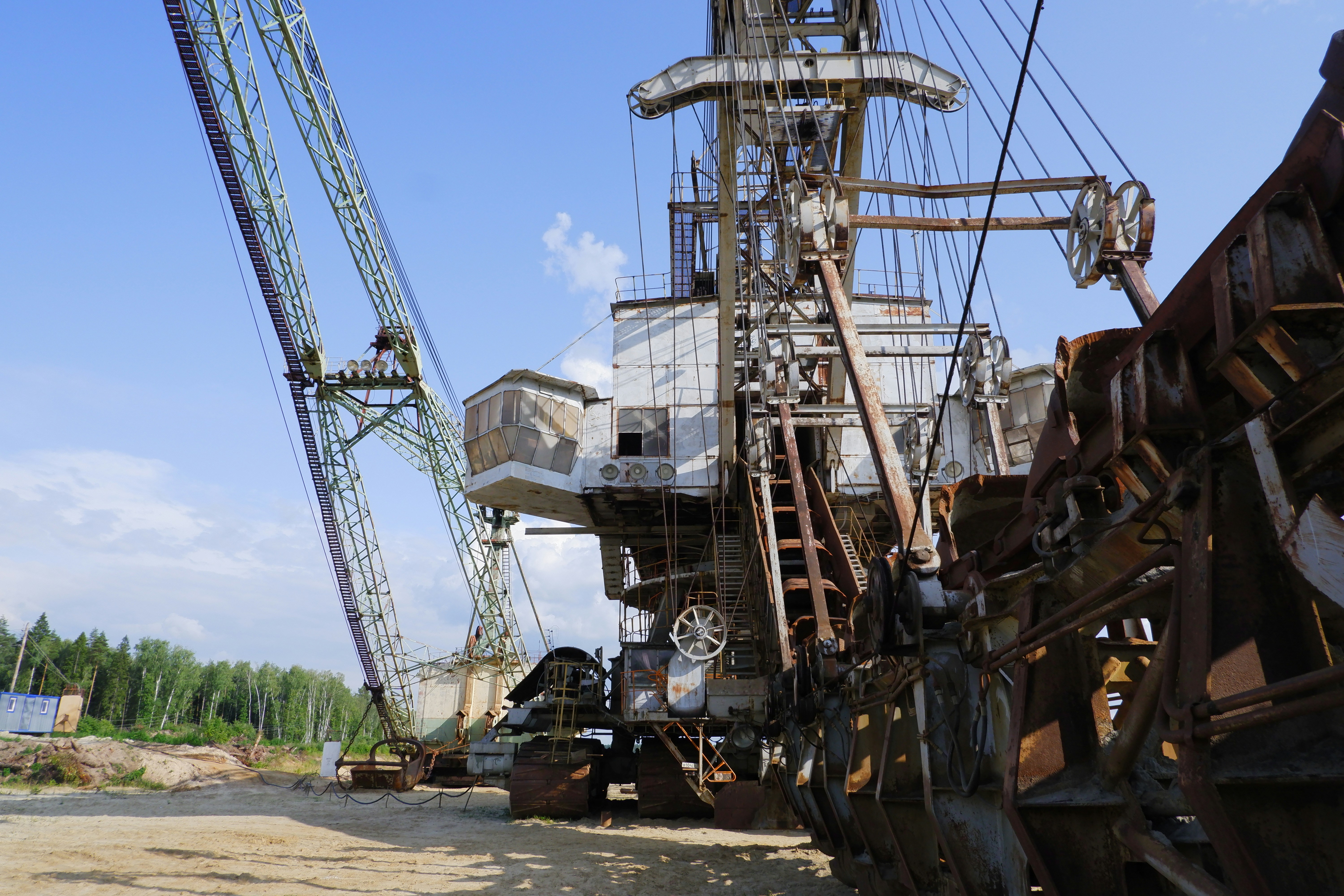 A massive excavator looms over the landscape, showcasing its intricate machinery against a backdrop of blue sky and greenery.