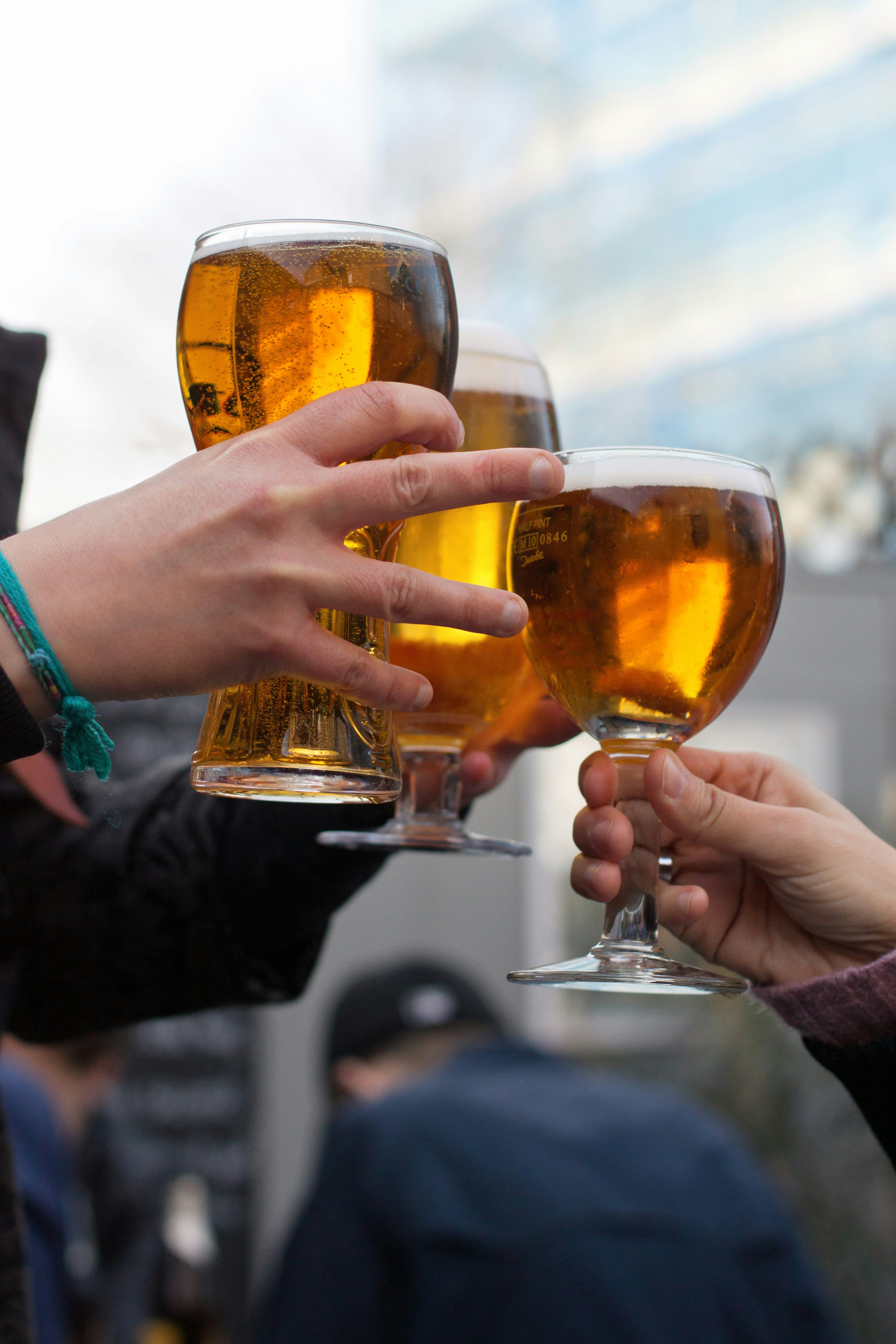 Four hands clinking glasses of golden beer in a lively outdoor setting, celebrating camaraderie and good times.