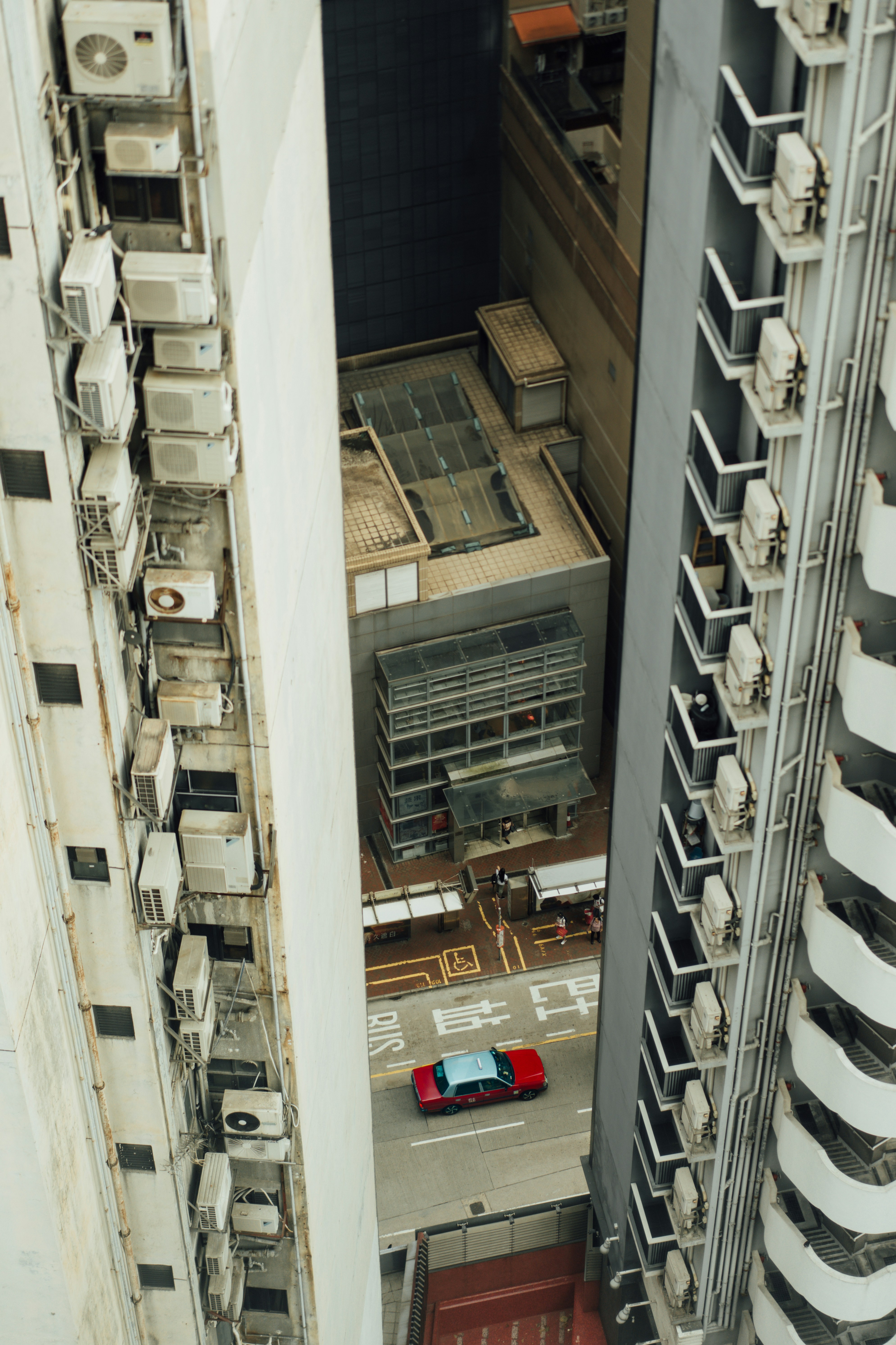Between Glass Giants: A Red Car Traverses a Narrow Urban Canyon