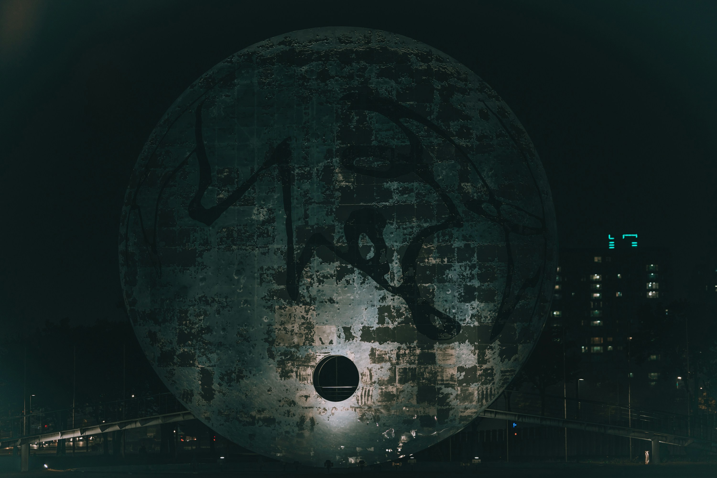 Graffiti-Splashed Sphere Illuminated at Night Over a Quiet Cityscape