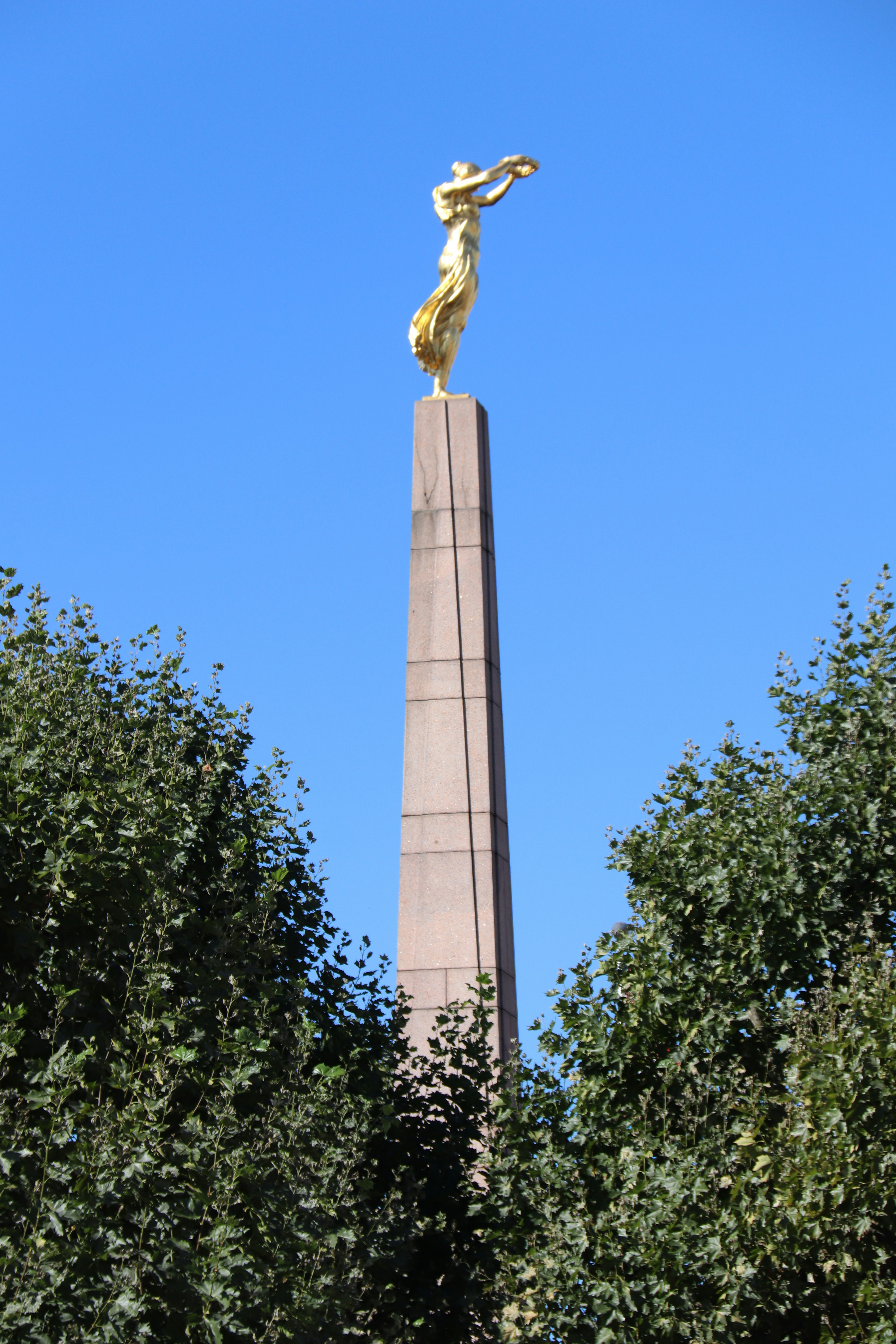 Gold Statue Reaching for the Sky Above a Stone Obelisk