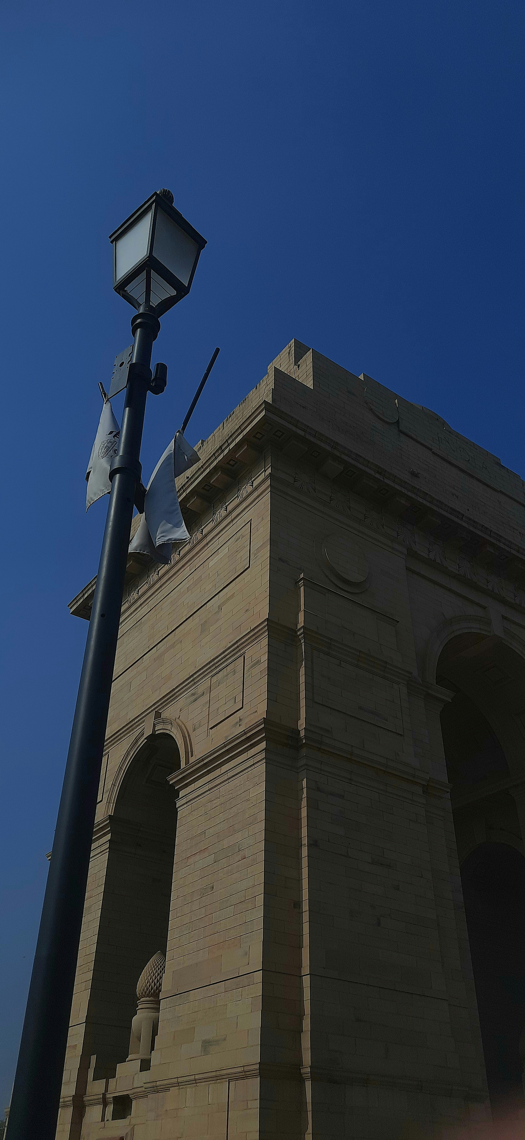 Architectural photograph showing a stone arch tower beside a tall street lamp against a deep blue sky. The image highlights masonry details and urban lighting.