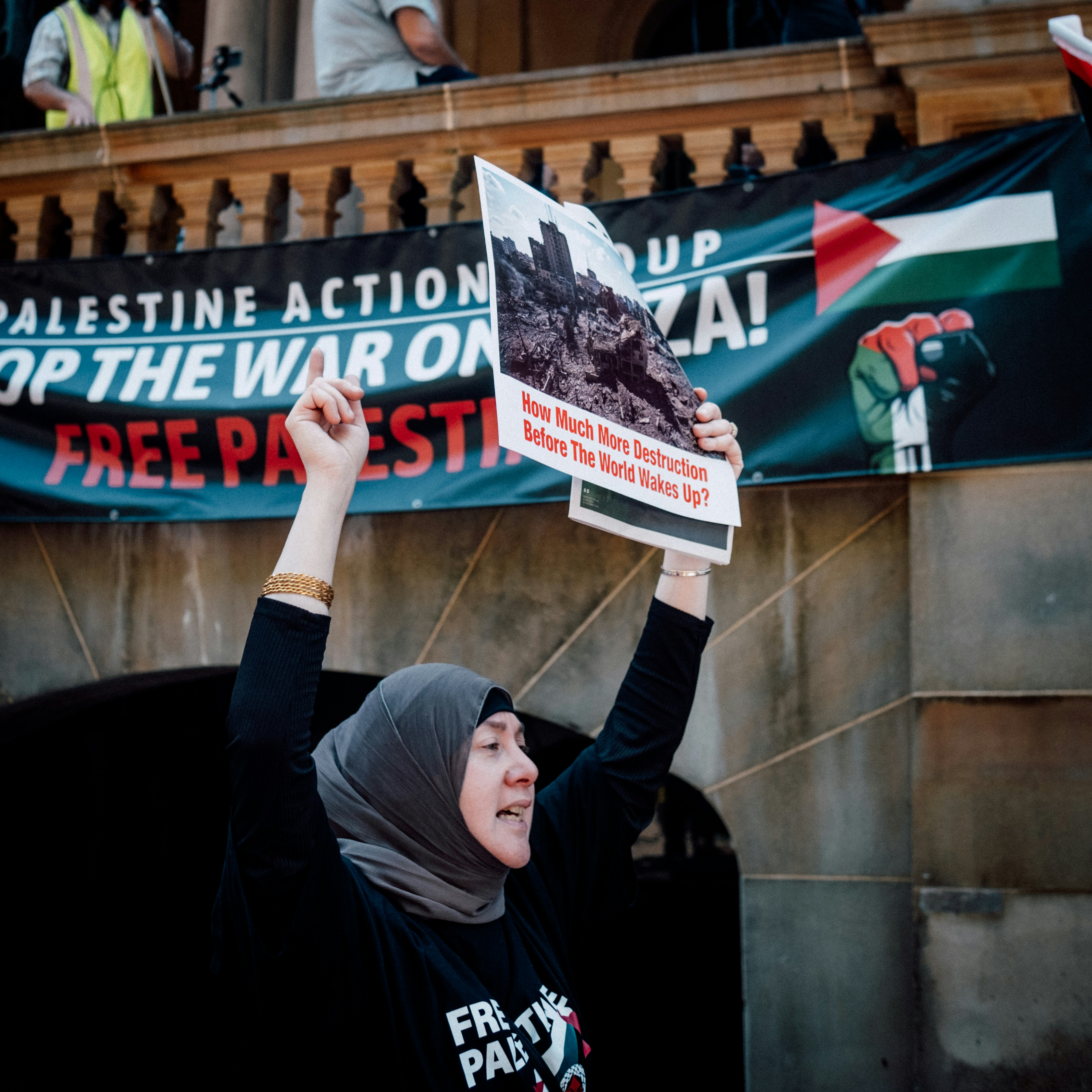 Raising a Message: A protester lifts a sign against a bannered backdrop