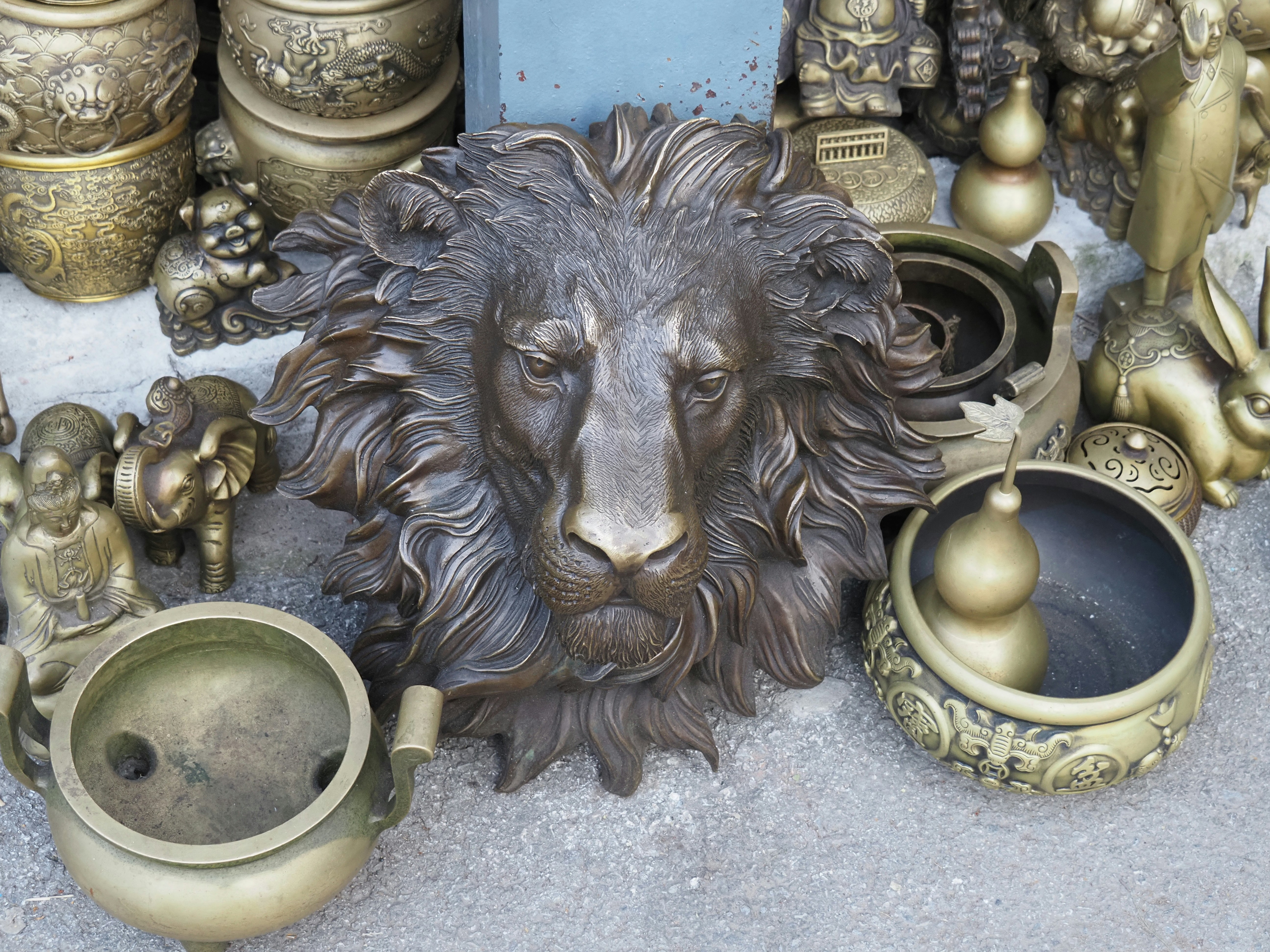Bronze lion head bust surrounded by small ornate vessels and trinkets in a display setting.