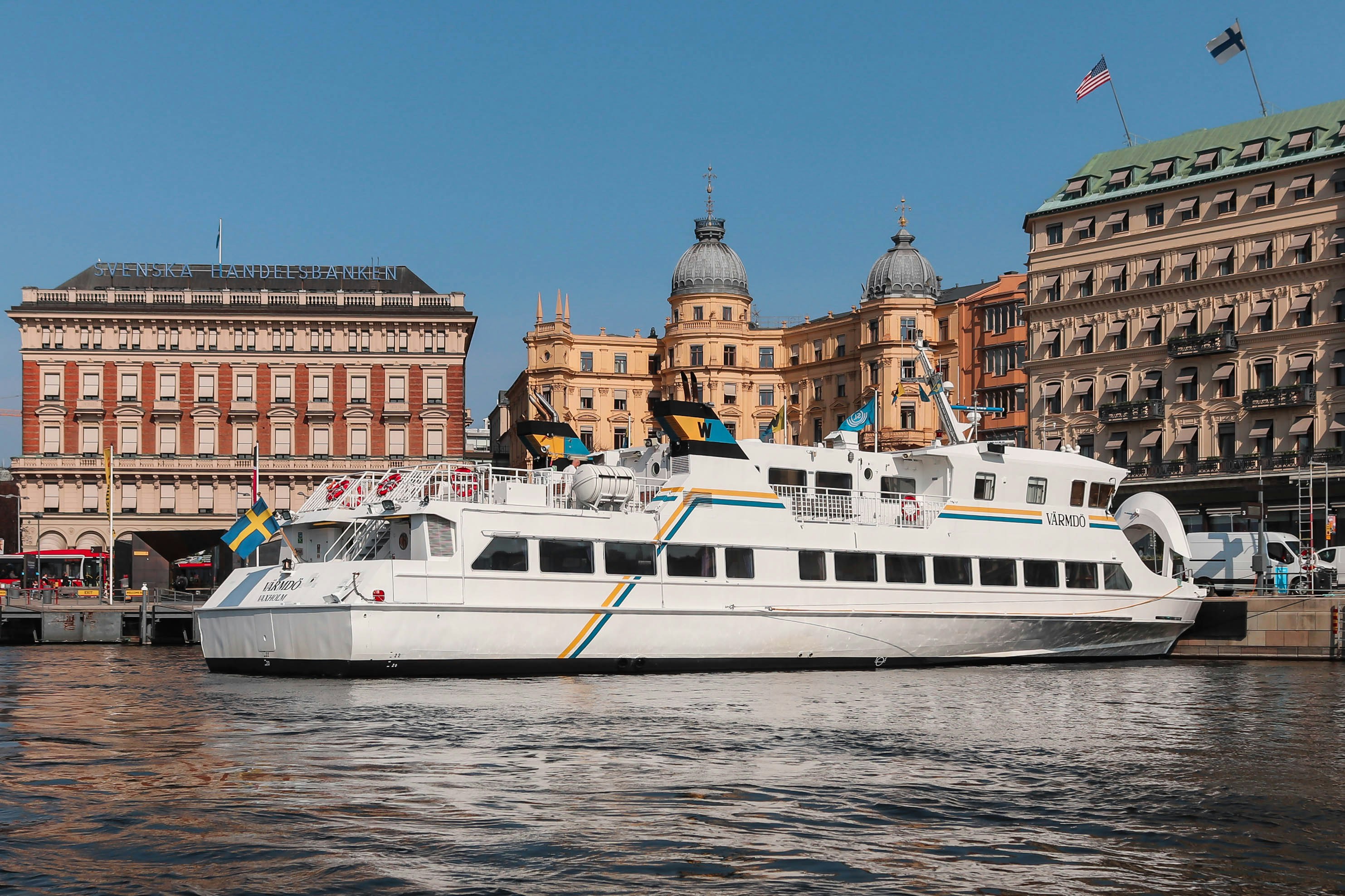 Large white boat docked in a city harbor with historic buildings in the background under a clear blue sky.