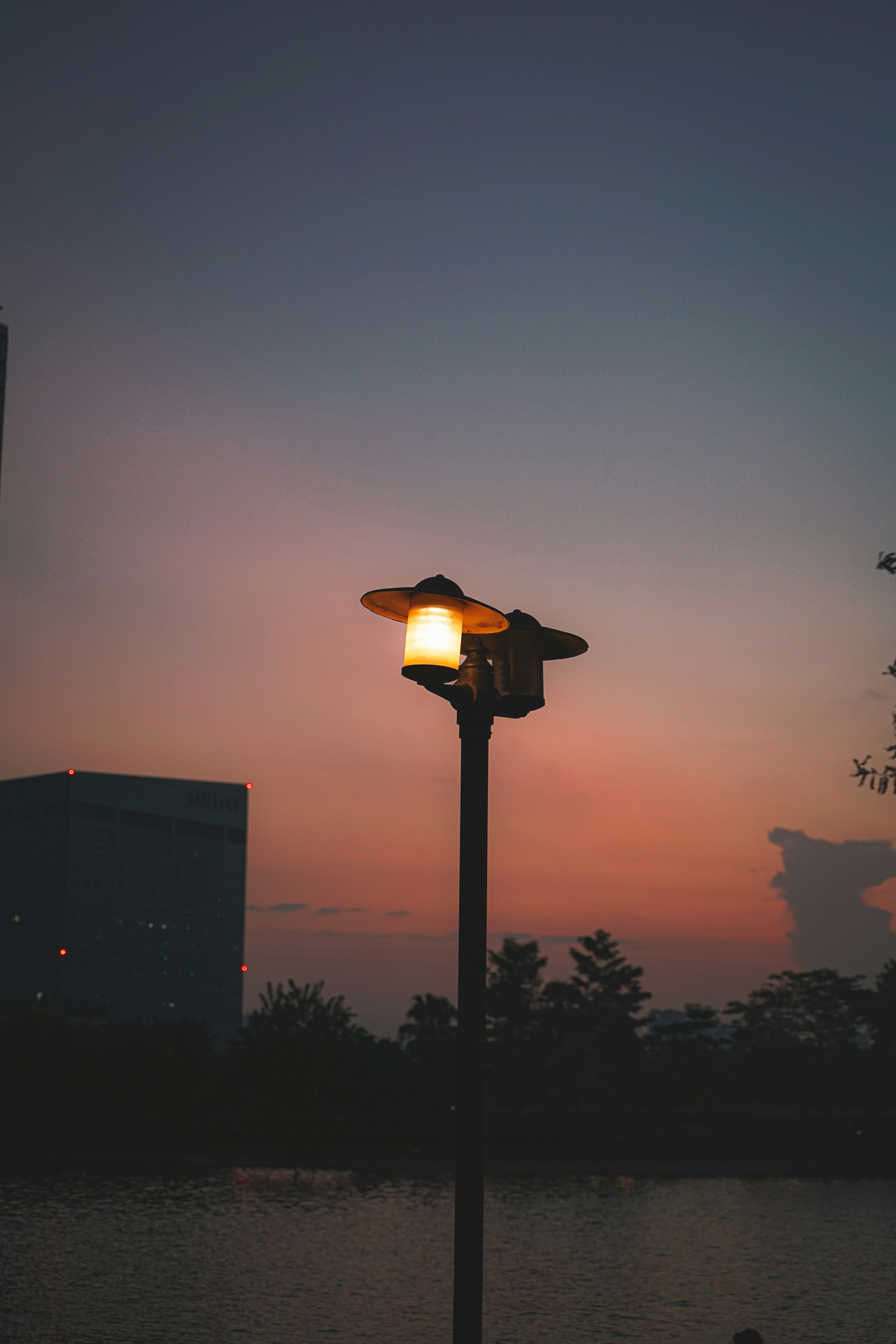Dusk Lantern Over Calm Water: a solitary streetlamp under a pastel sky