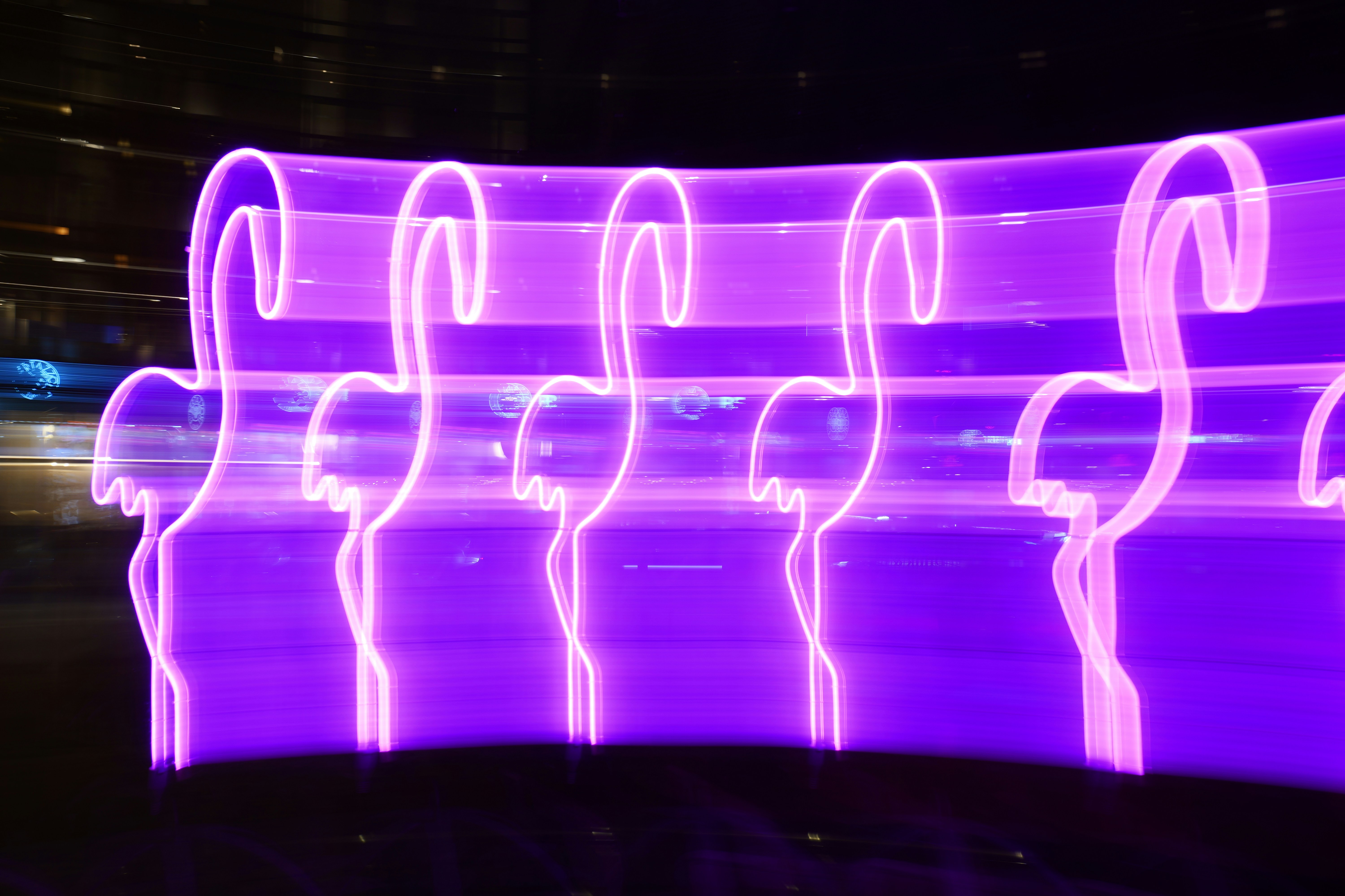 Long-exposure photograph of neon purple flamingo-shaped light trails arching across a dark space.