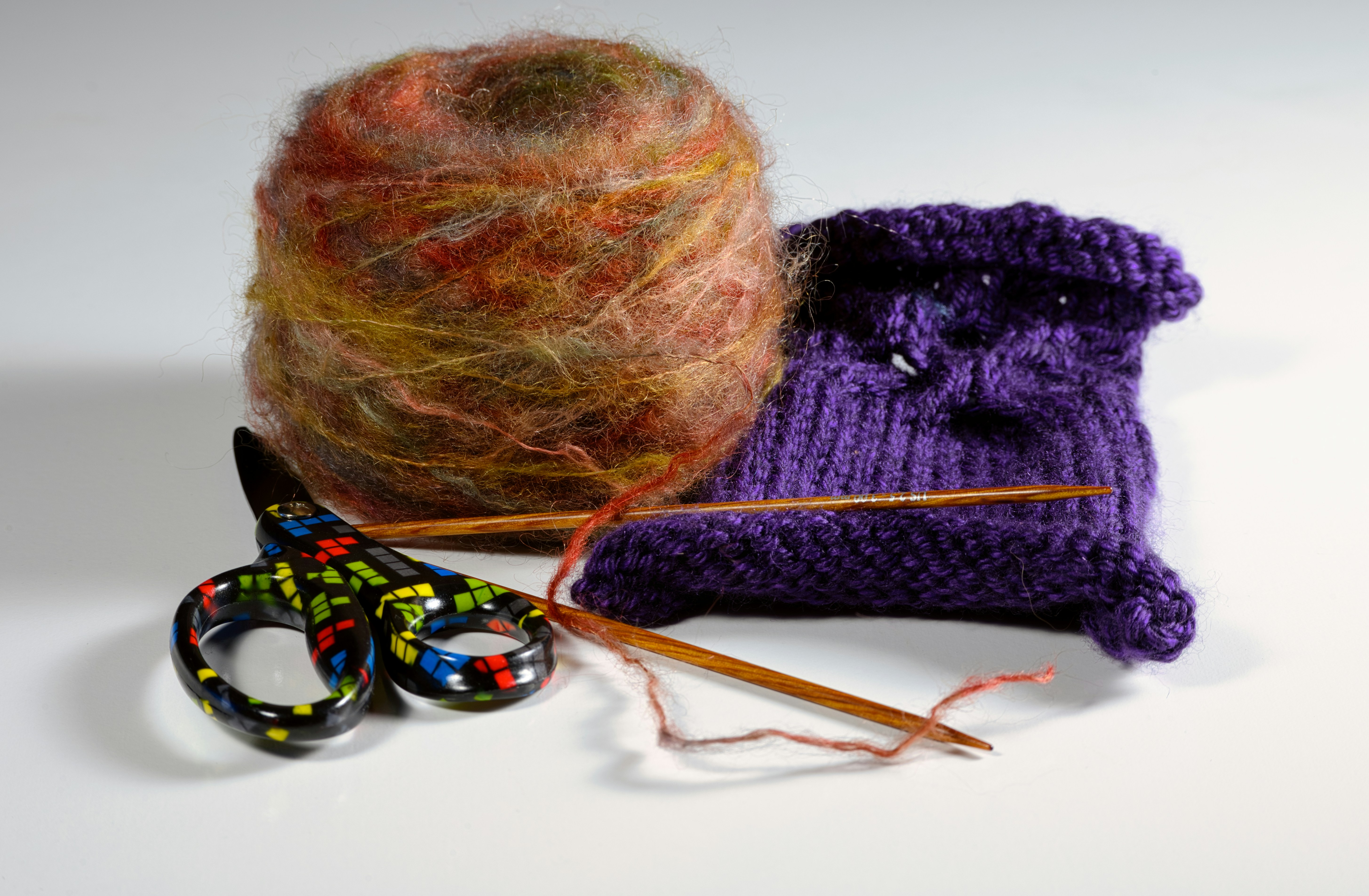 Colorful yarn ball, knitting needles, and scissors arranged on a clean surface, showcasing the essentials for a cozy crafting session.