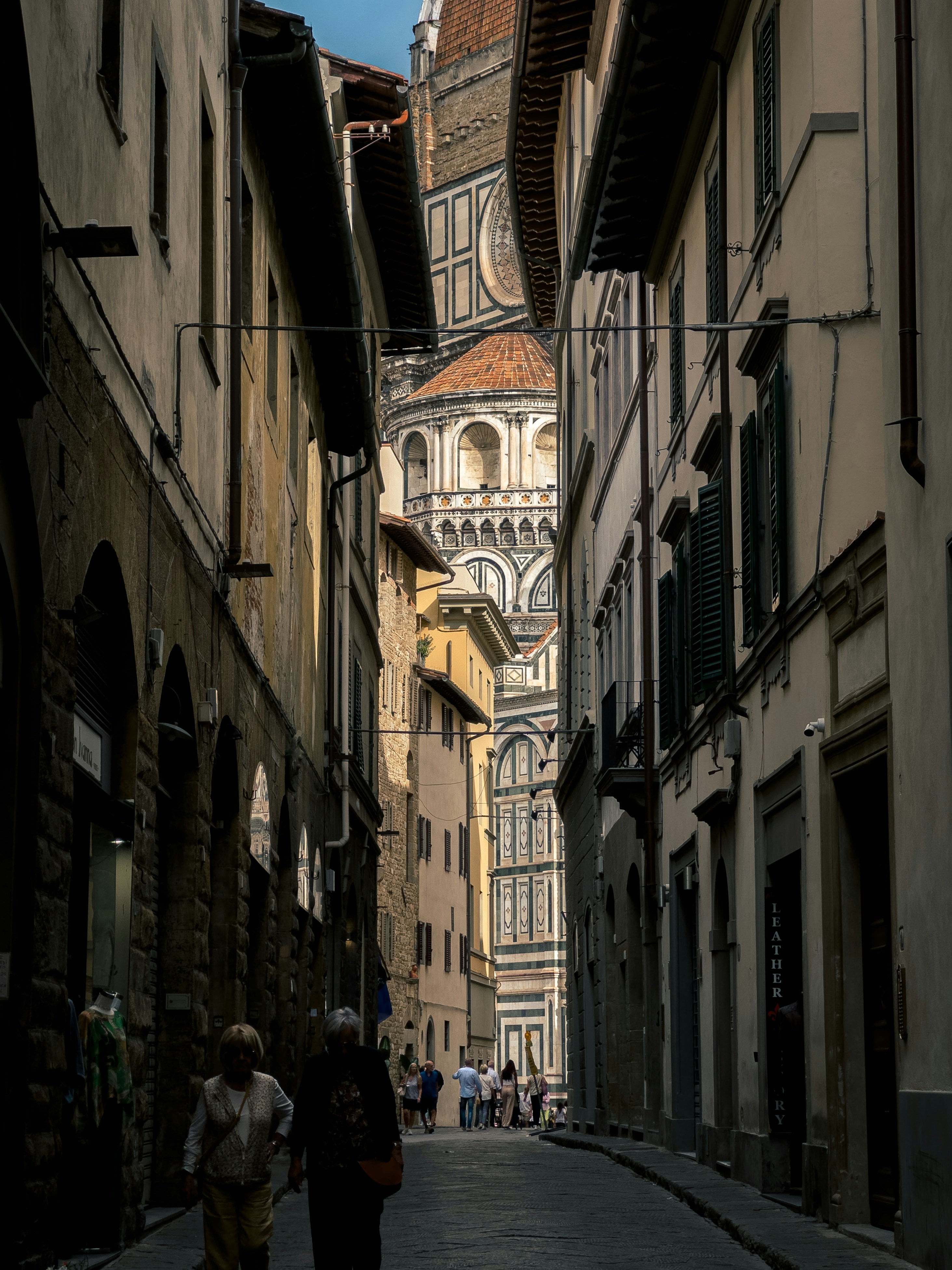 Narrow street in Florence leading to the intricate façade of the Duomo, framed by historic buildings. A blend of everyday life and iconic architecture.