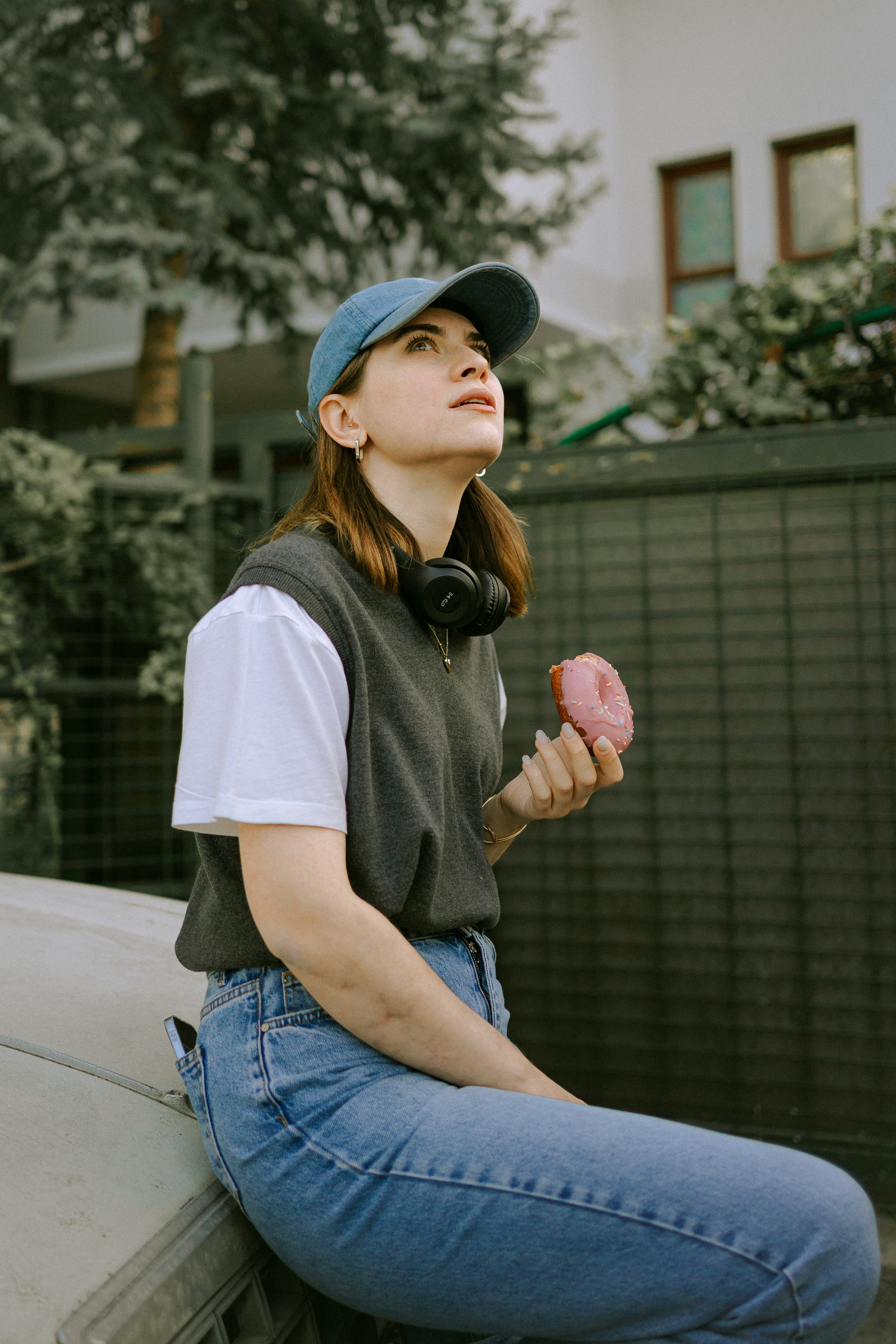 A woman sitting on a ledge eating a donut photo – Free Pants Image on ...