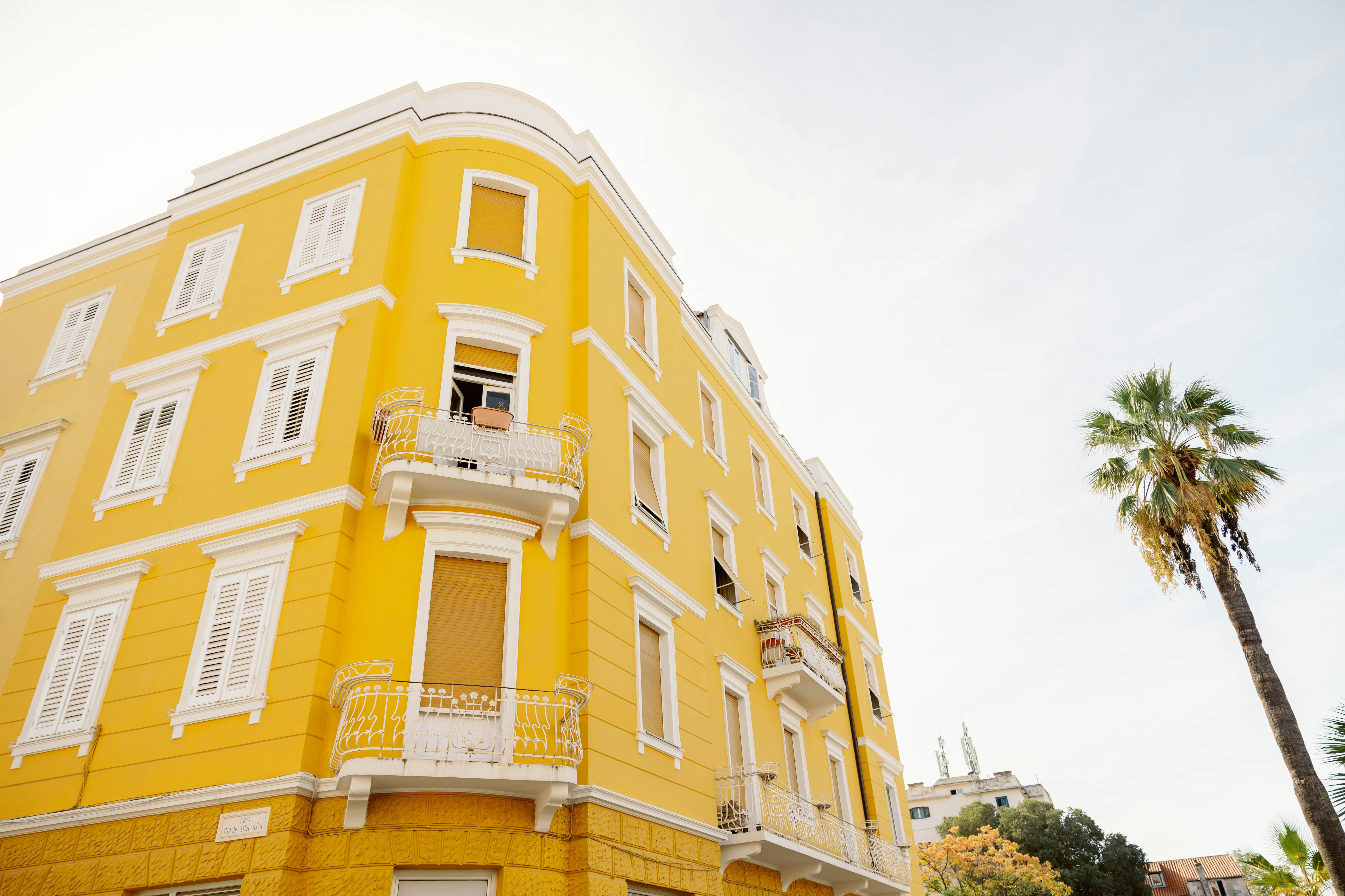 A tall yellow building with white windows and balconies photo – Free ...