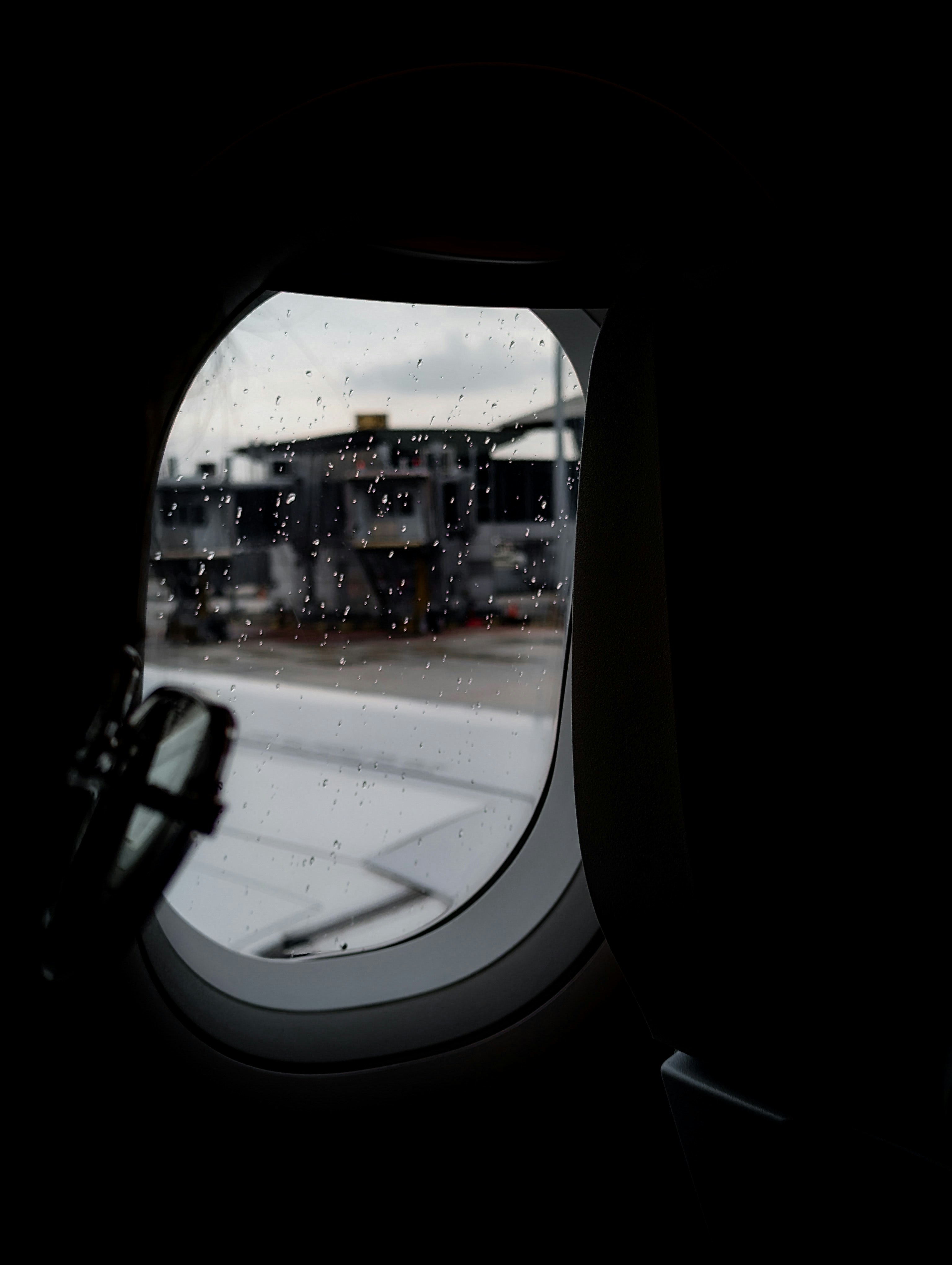 Rain-Dotted Pane: A Dim Airport Scene Framed by a Plane Window