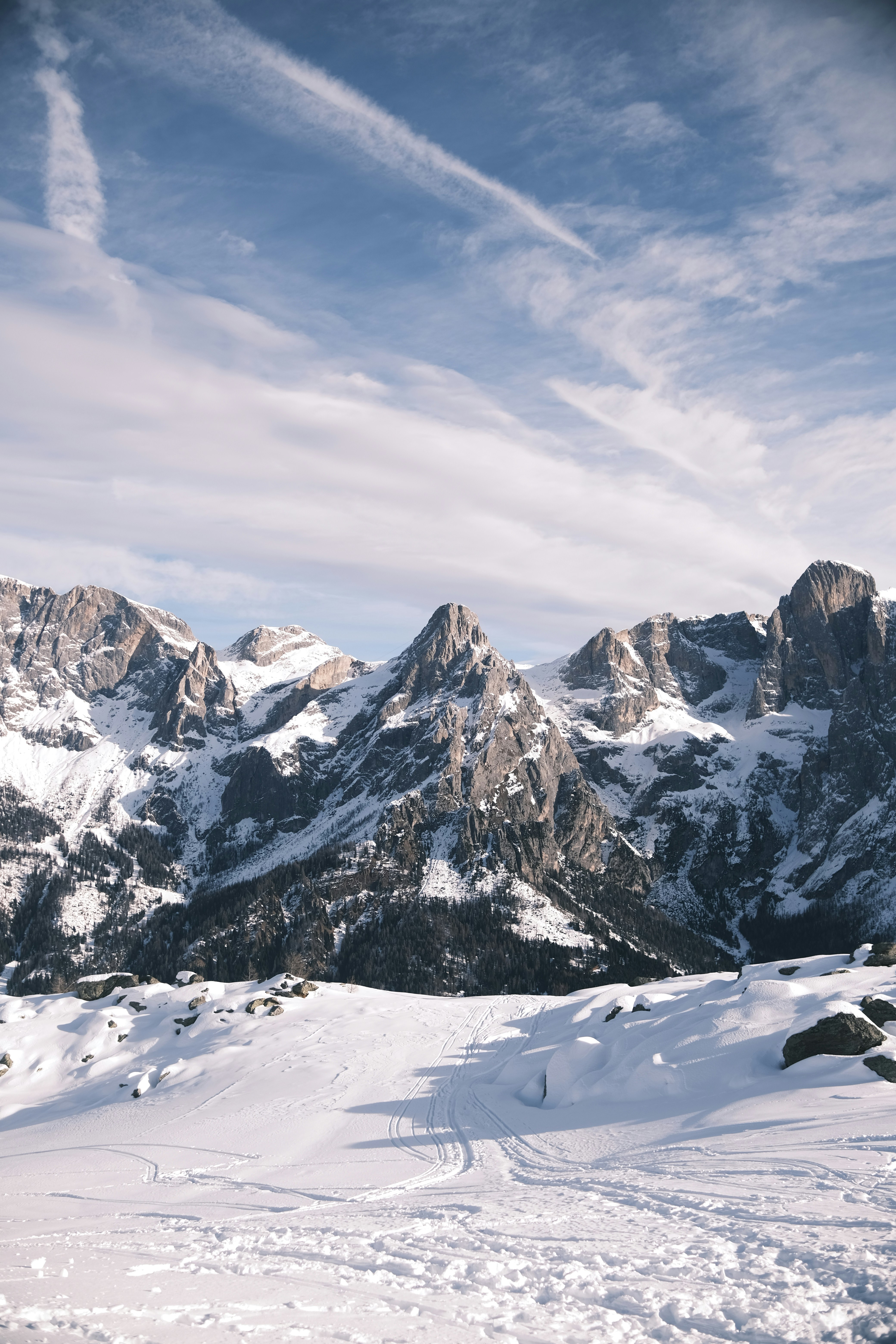 Snow-covered mountain range under a clear blue sky with wispy clouds.