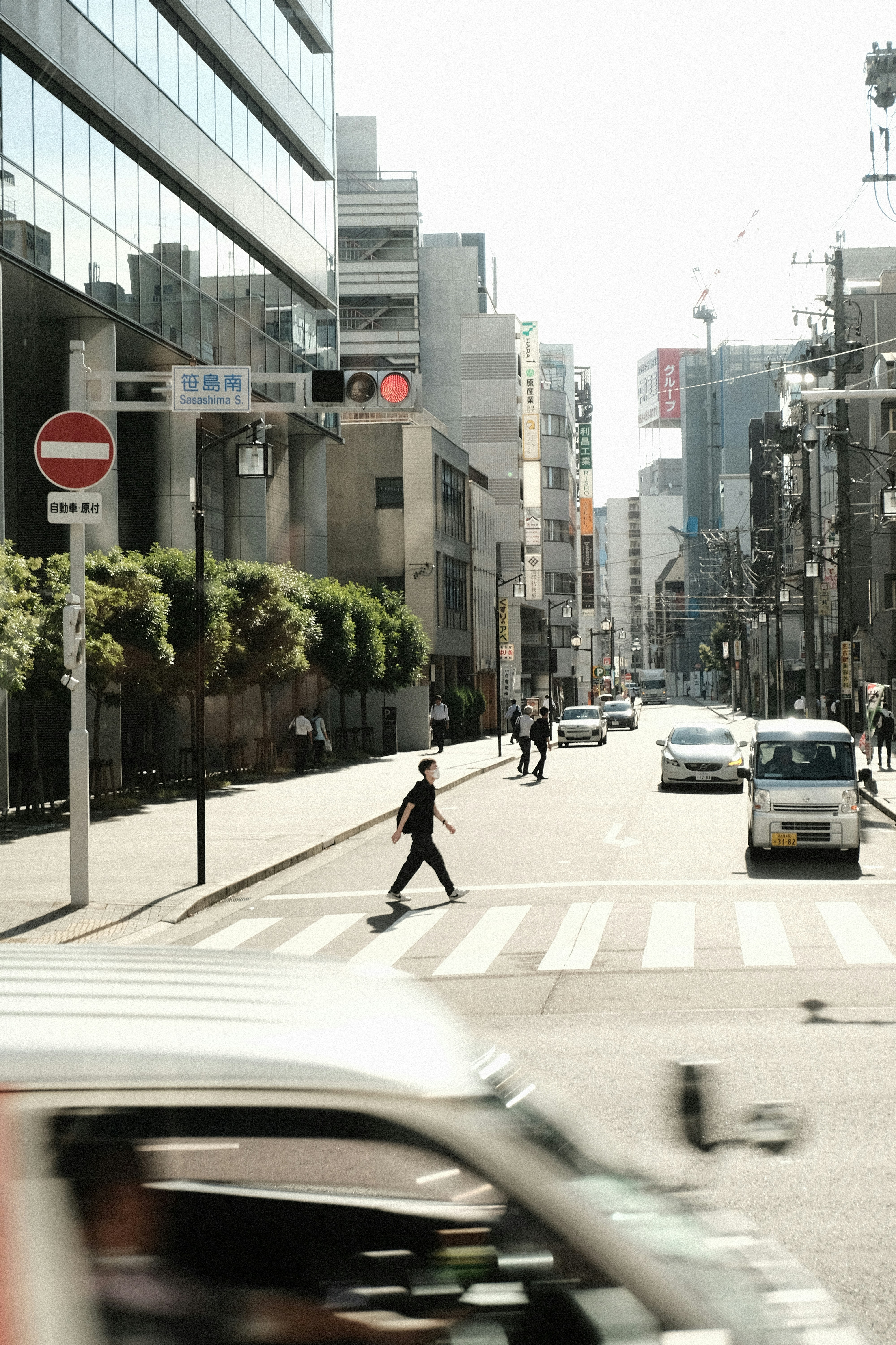 A pedestrian crosses a bustling city street, framed by modern architecture and traffic signals. The scene captures the dynamic essence of urban life.