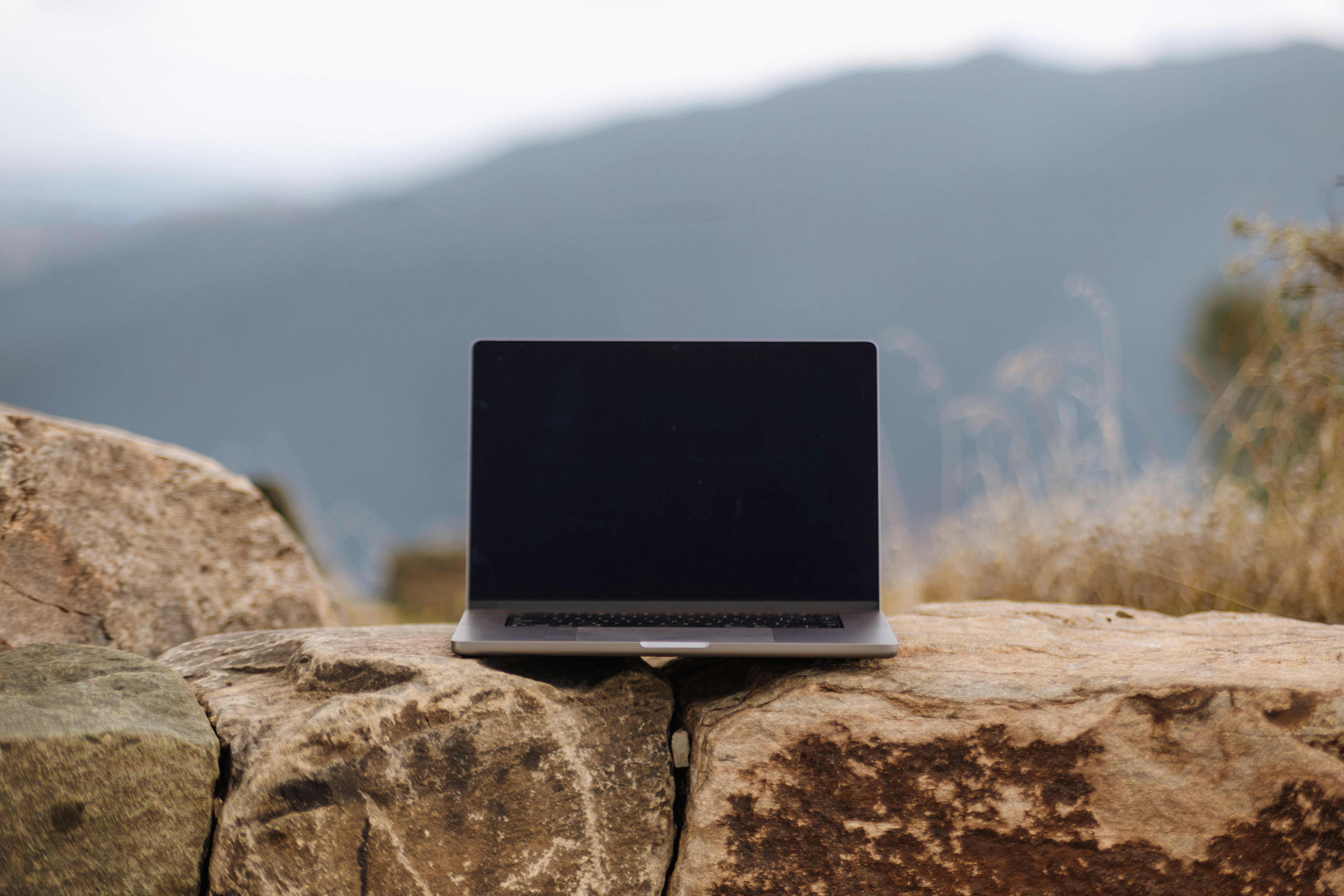 Laptop Resting on a Stone Wall Against a Mountainous Horizon