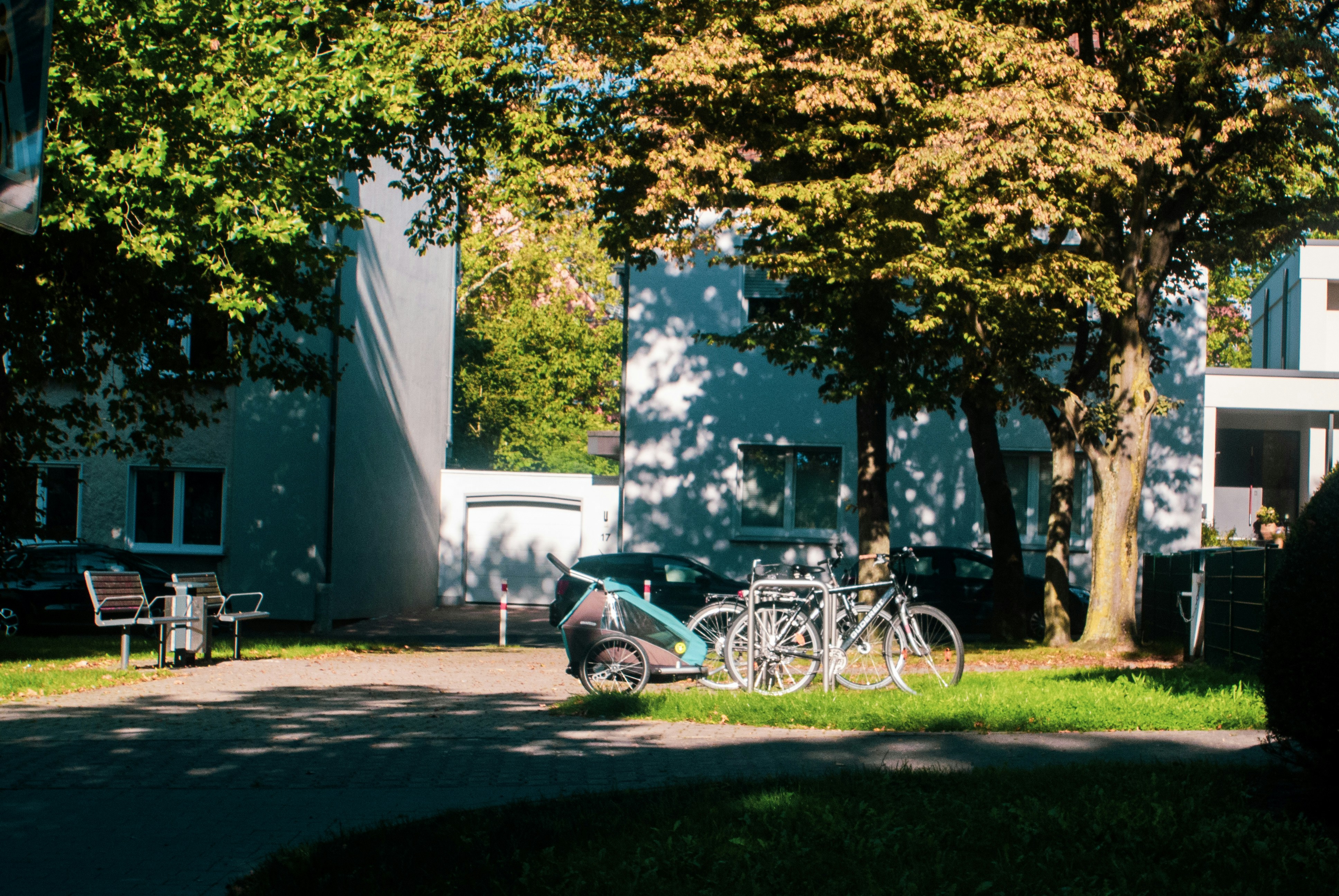 Bicycles parked near benches under sunlit trees in a peaceful courtyard.
