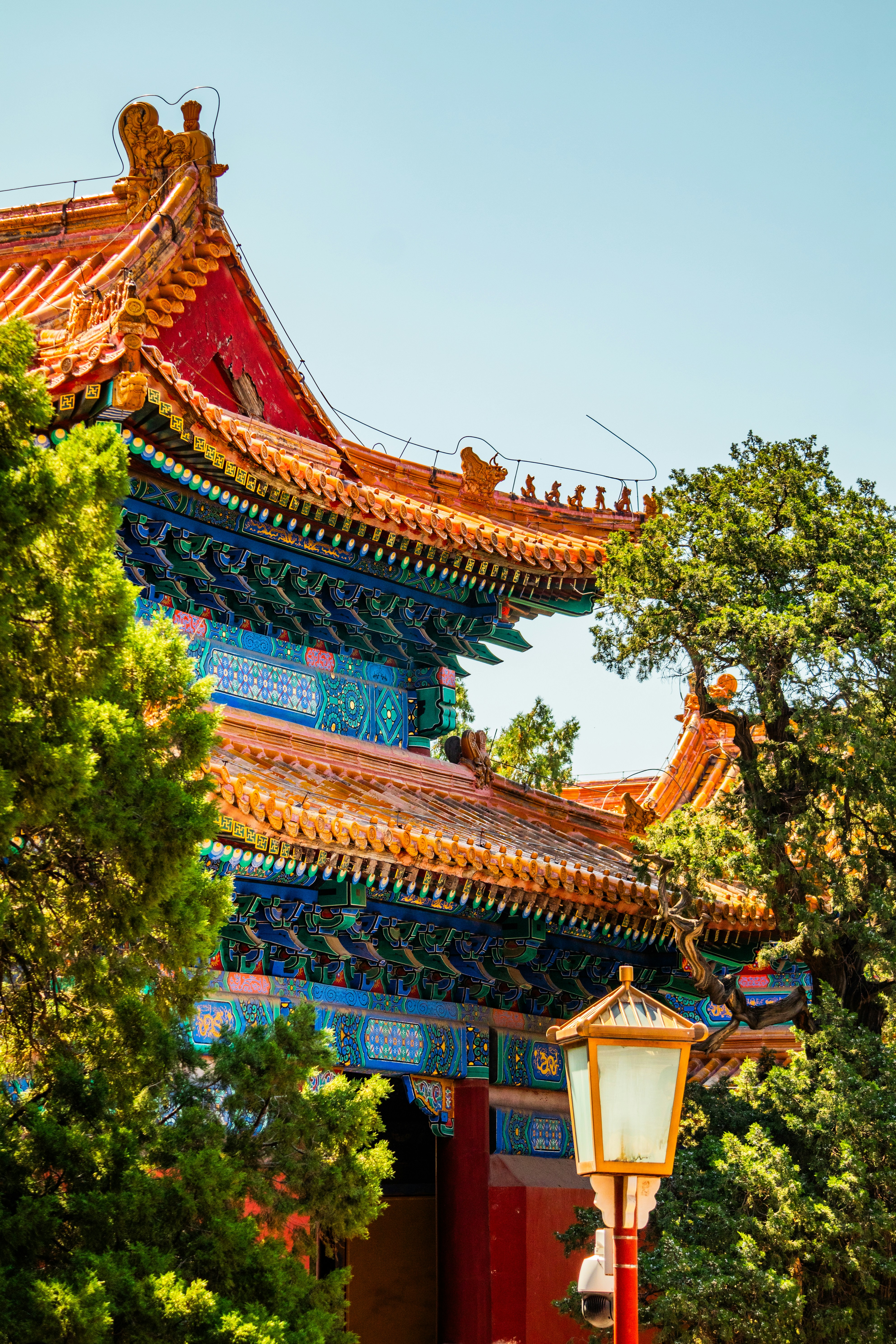 Vibrant traditional architecture showcasing ornate roof details and colorful decorations, framed by lush greenery and a lamppost.