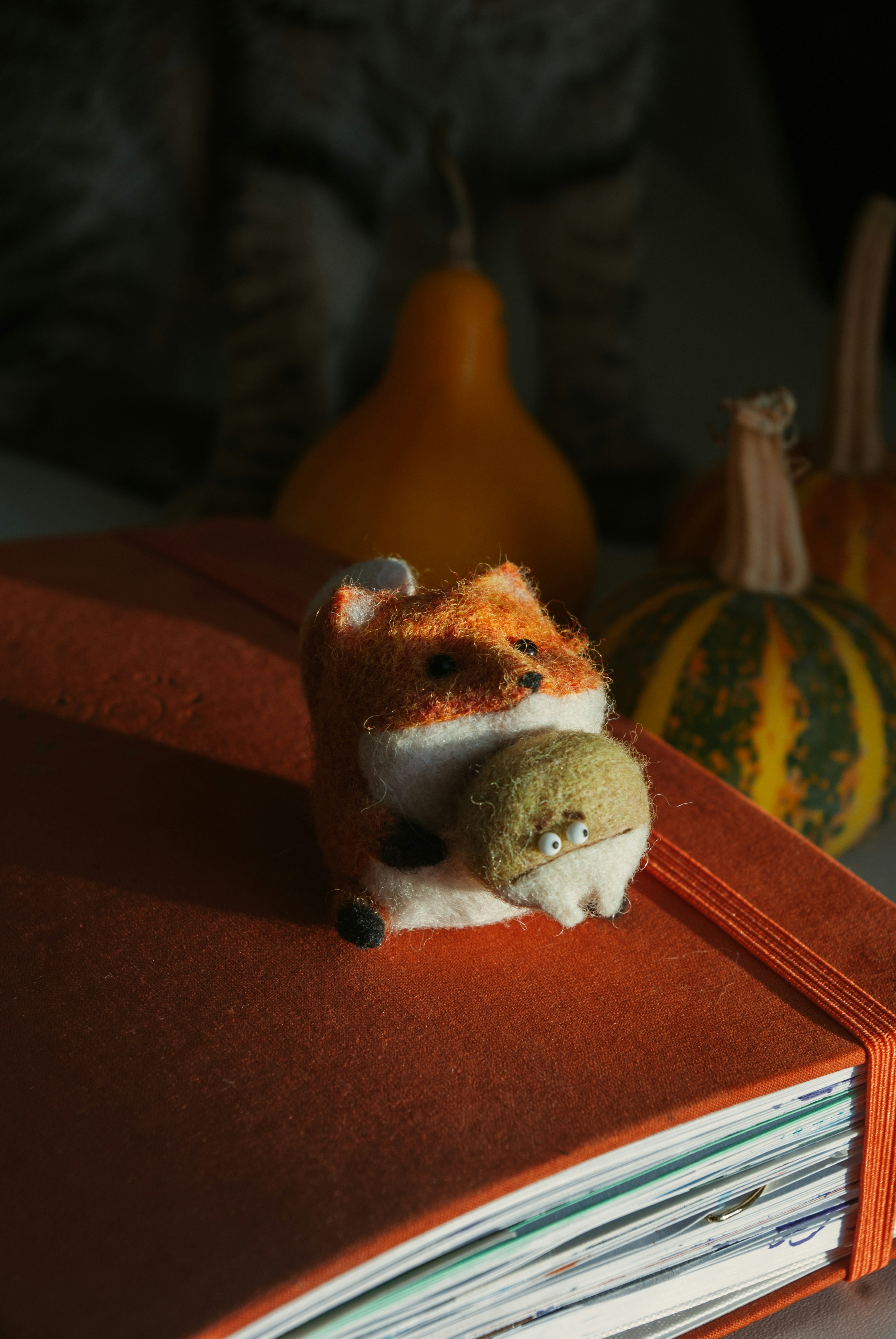 Tiny Felted Fox Perches on a Crimson Notebook Beneath Autumnal Light