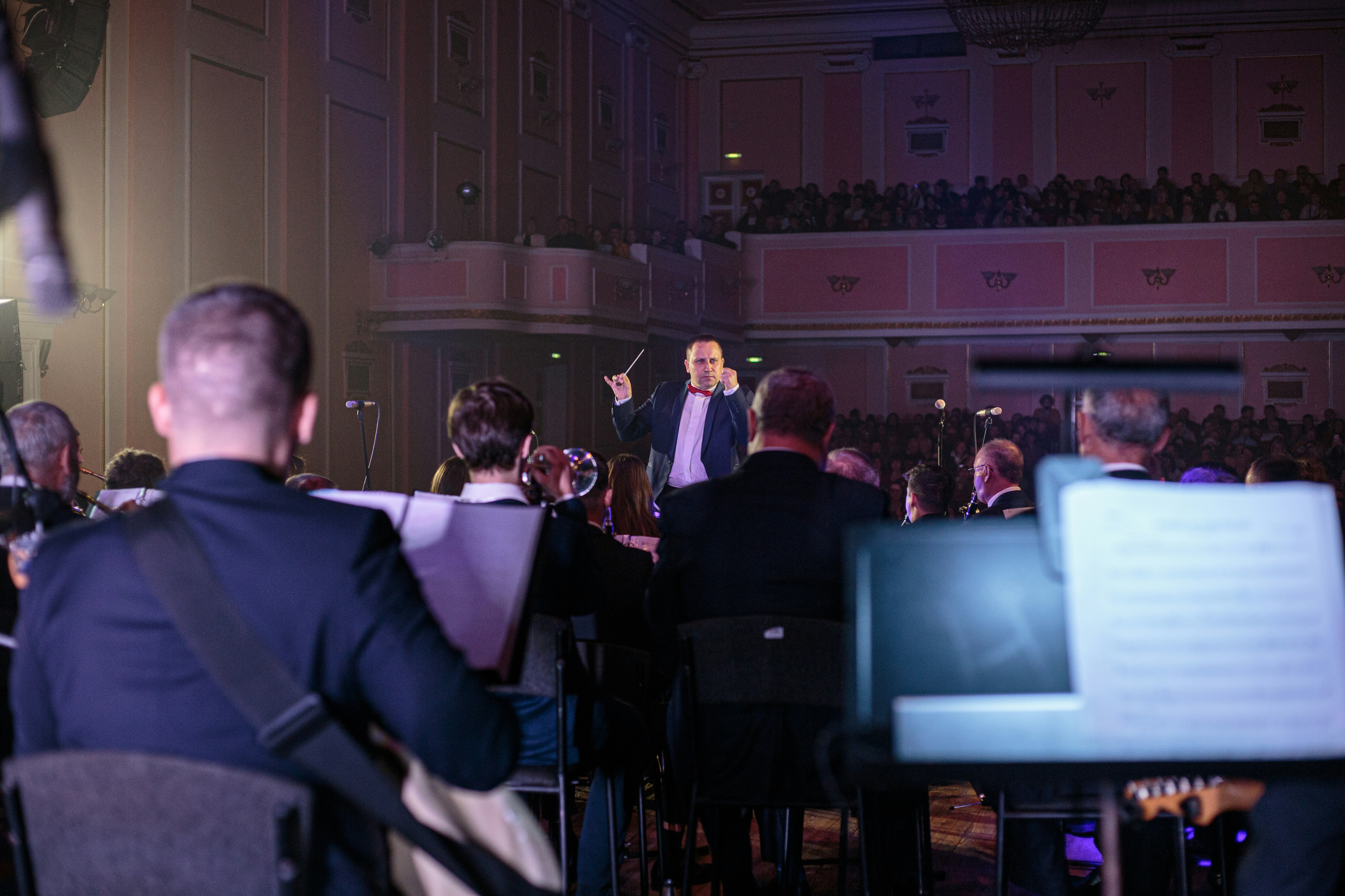 A conductor and orchestra performing in front of an audience photo ...