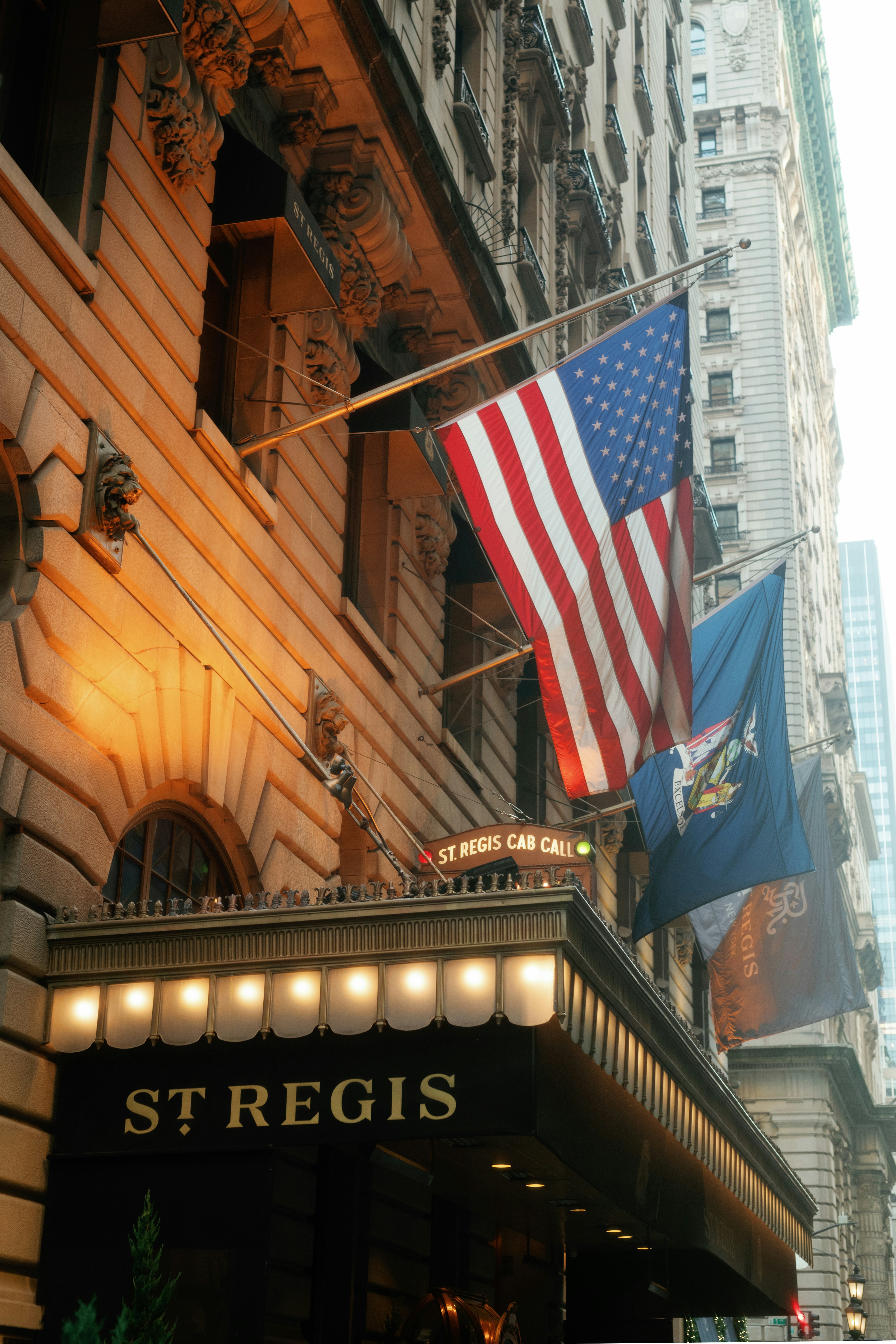 Historic St. Regis Hotel entrance adorned with American and state flags, showcasing architectural detail and urban charm.