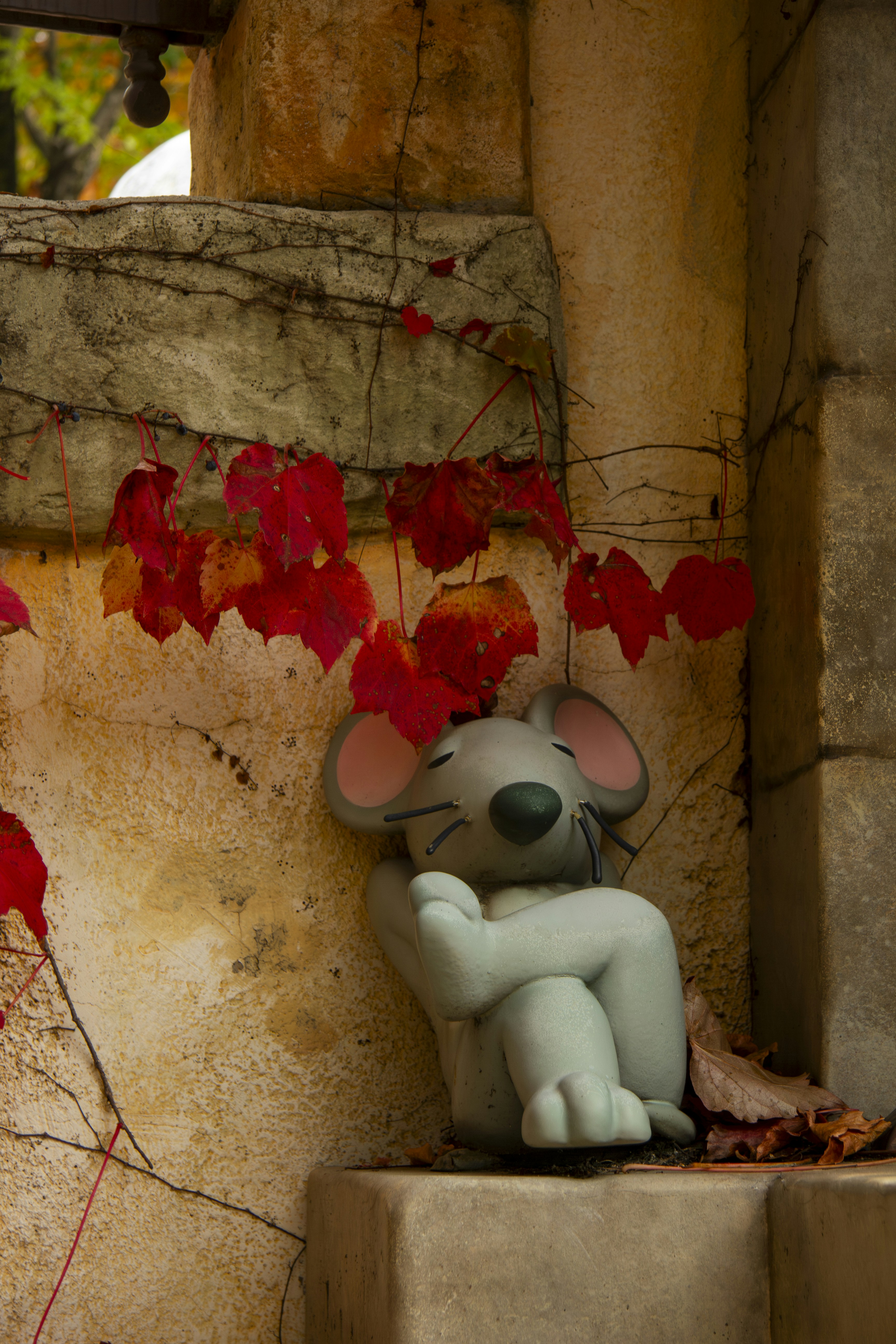 Crimson Vines Embrace a Quiet Mouse Statue on Weathered Stone