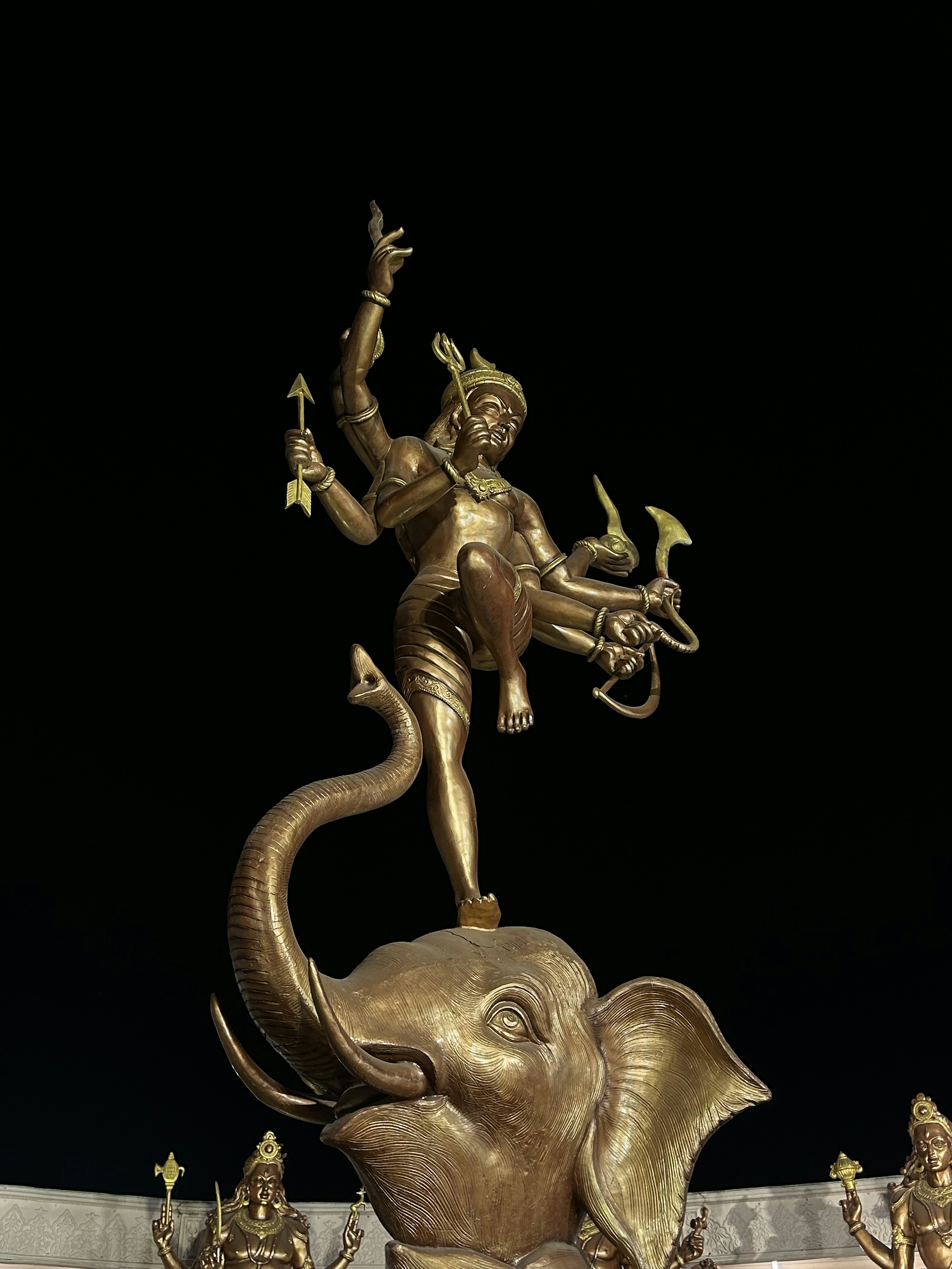 A bronze sculpture of Shiva Nataraja dancing atop an ornate elephant-head pedestal against a dark backdrop.
