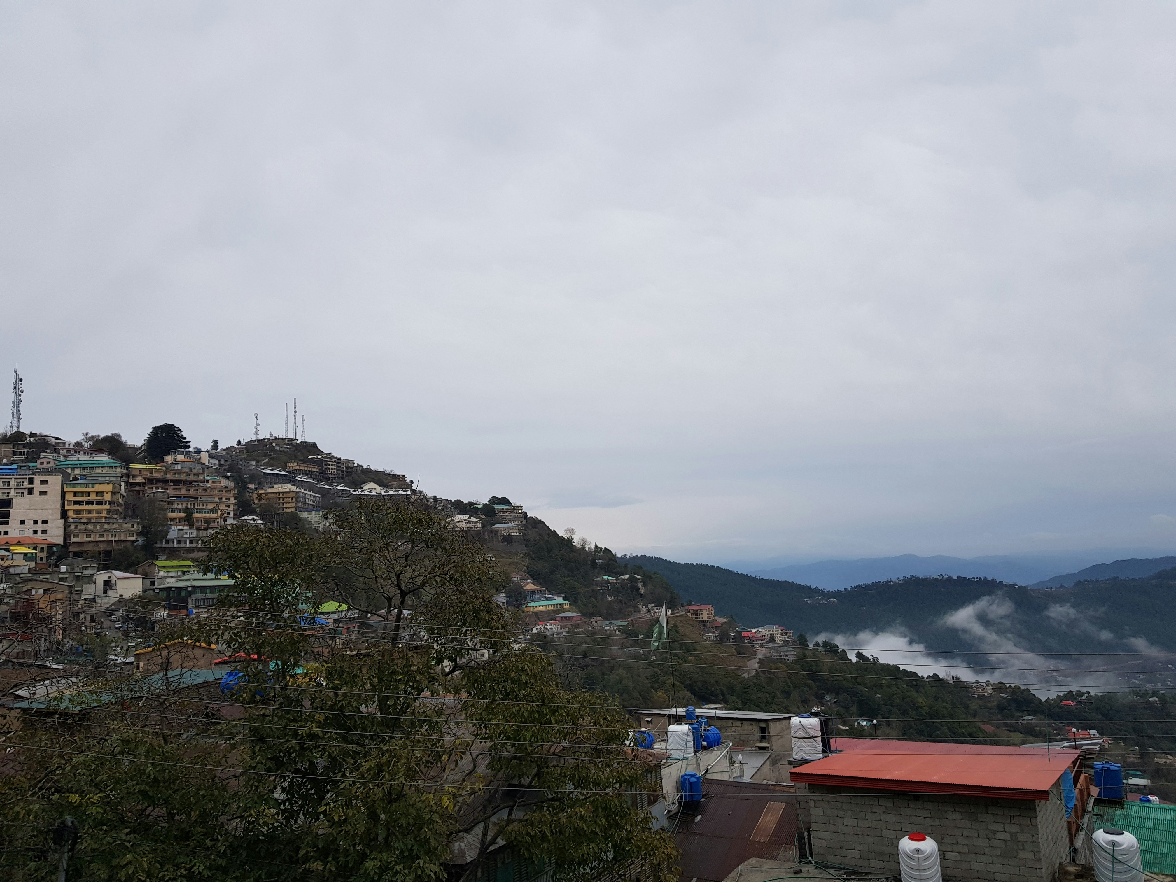 Hillside village overlooking mist-covered valleys under a cloudy sky.