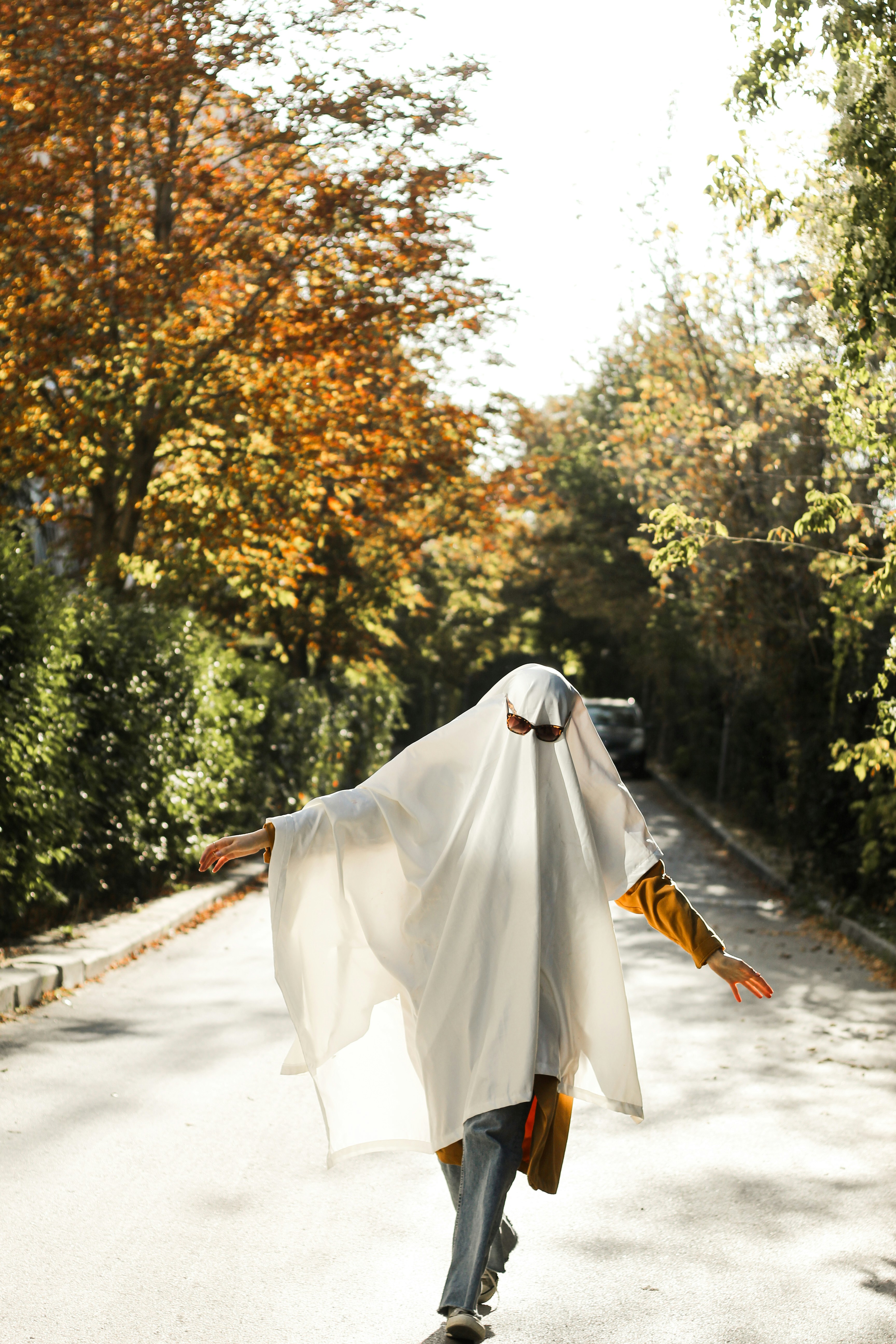 White-enshrouded Figure Crossing a Sunlit Autumn Road