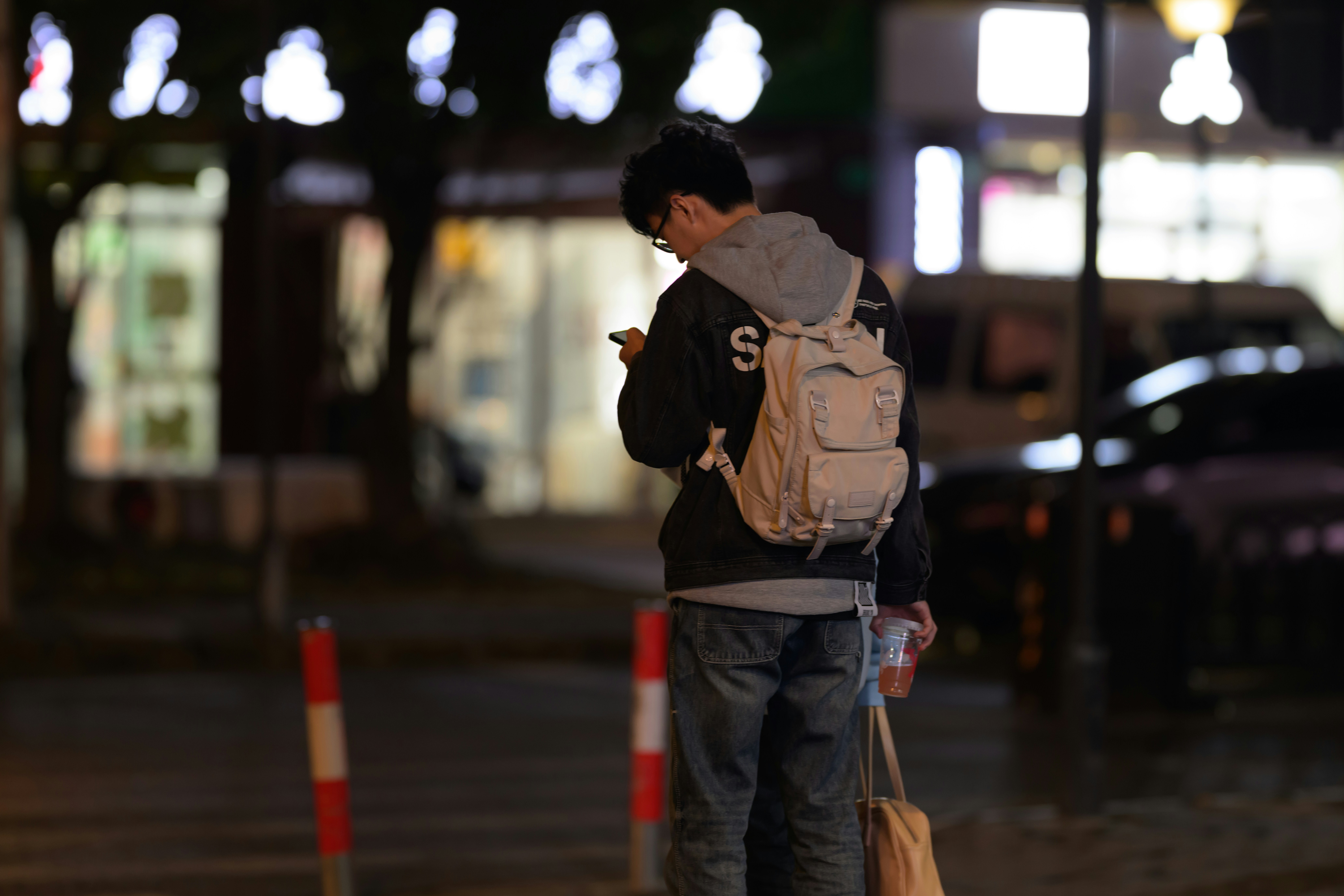 Neon Glow, Quiet Steps: A lone traveler pauses with a phone under city lights