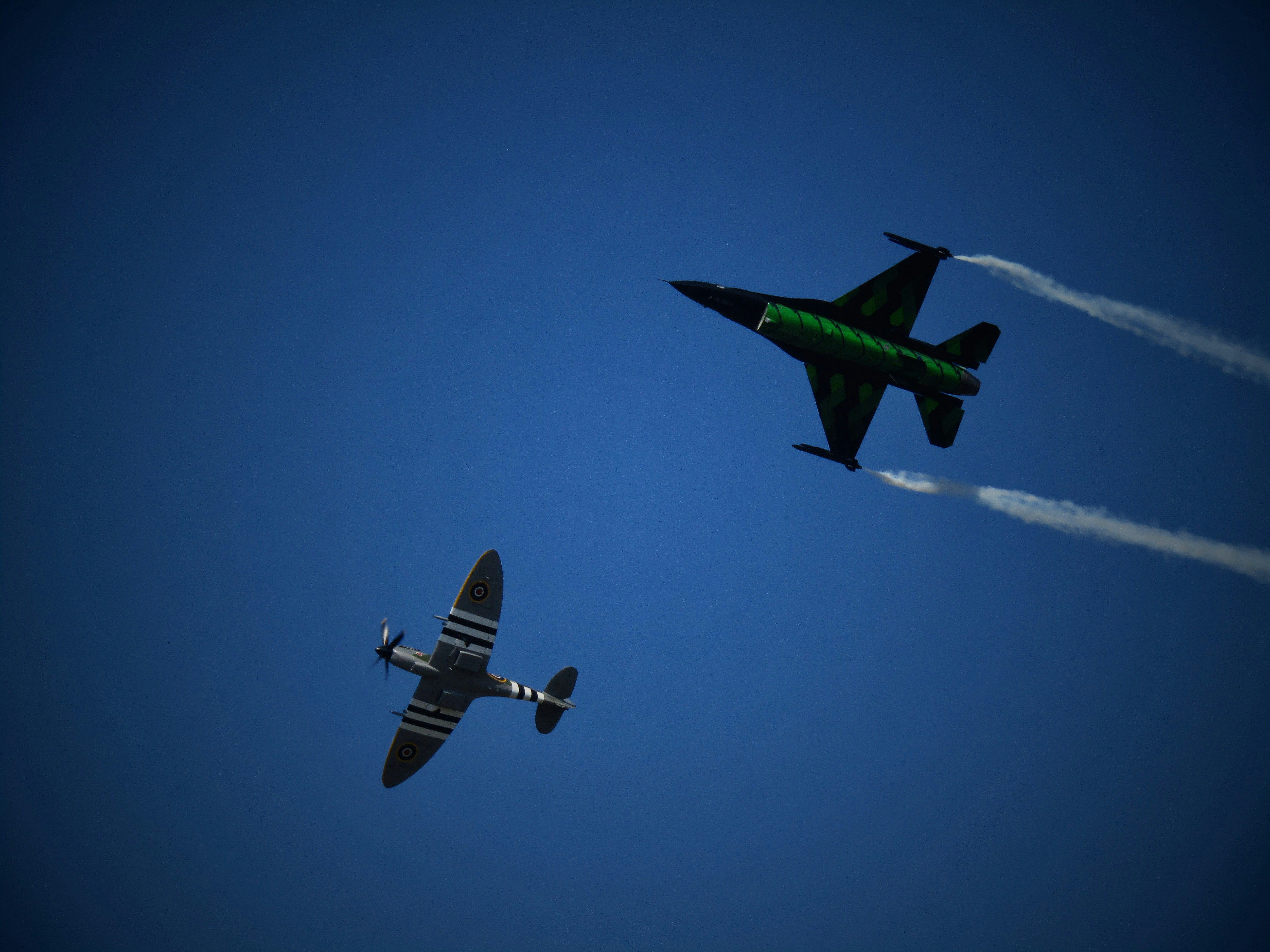 Skybound Duo: A Green Jet and Silver Spire Slice Through Cerulean Air