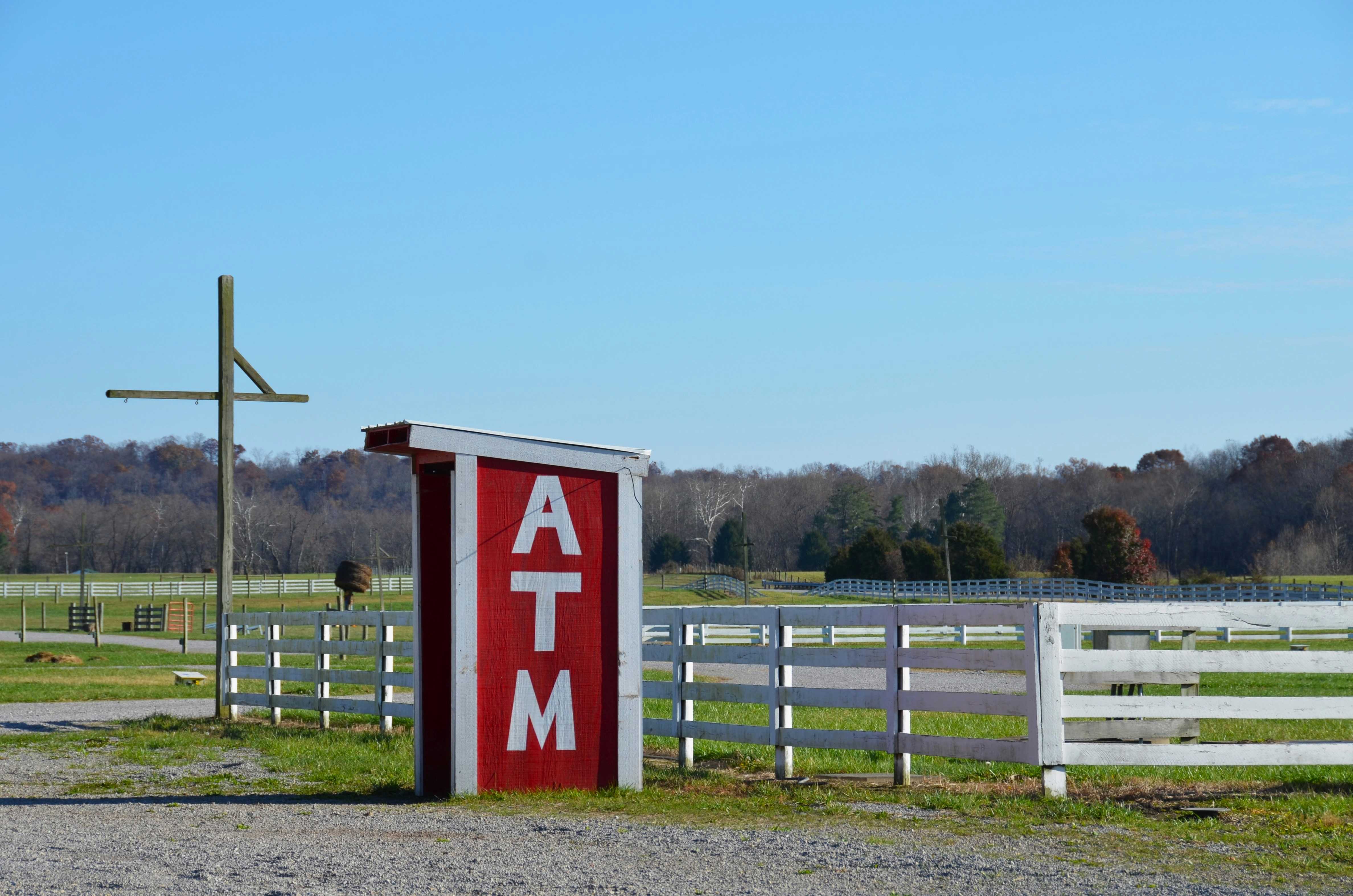 A red and white atm sign next to a white fence photo – Free Outdoors ...
