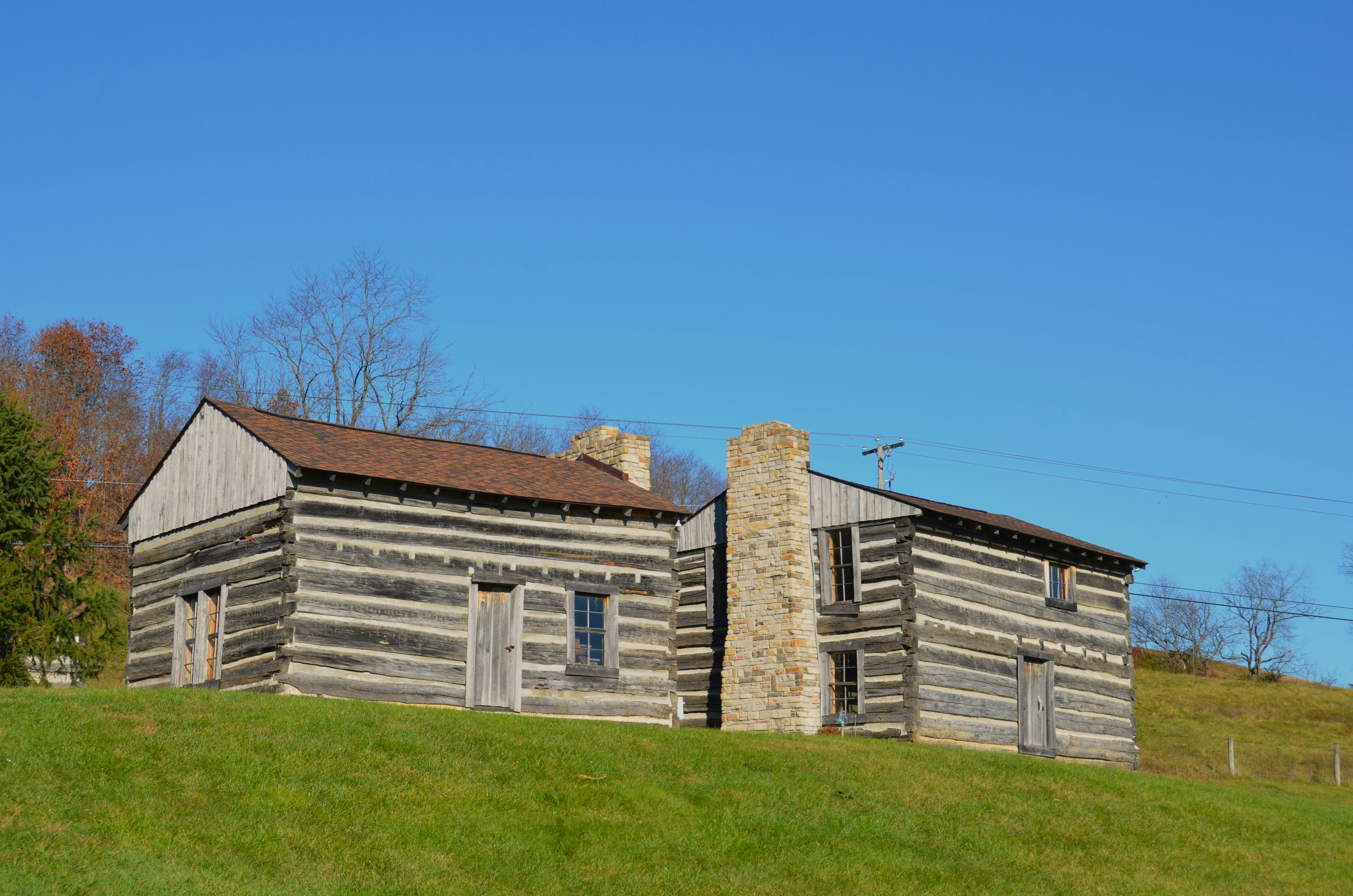 Two historic log cabins stand proudly on a grassy hill, showcasing traditional architecture against a clear blue sky.