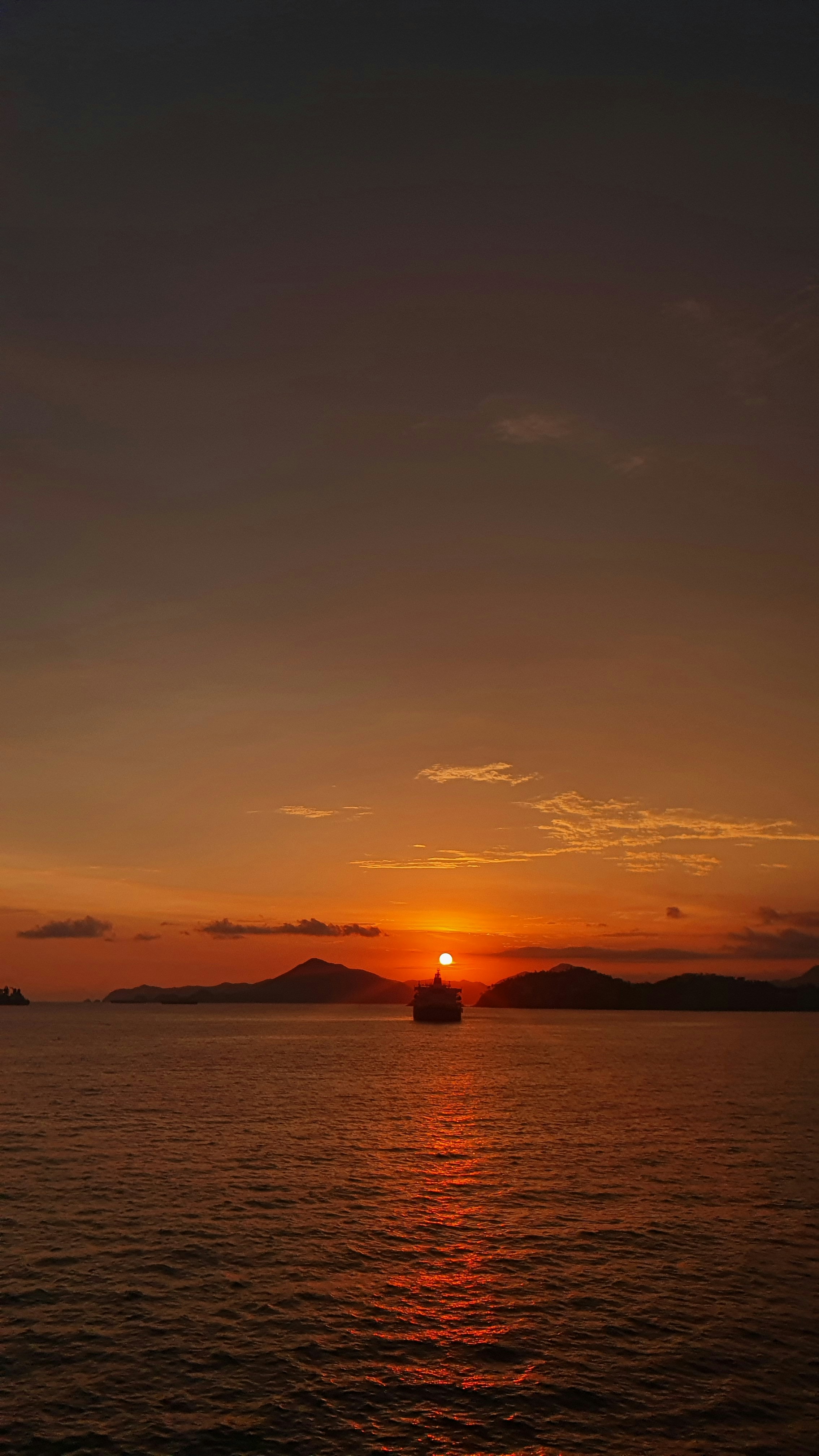 Sunset over ocean with mountains silhouetted against an orange sky.