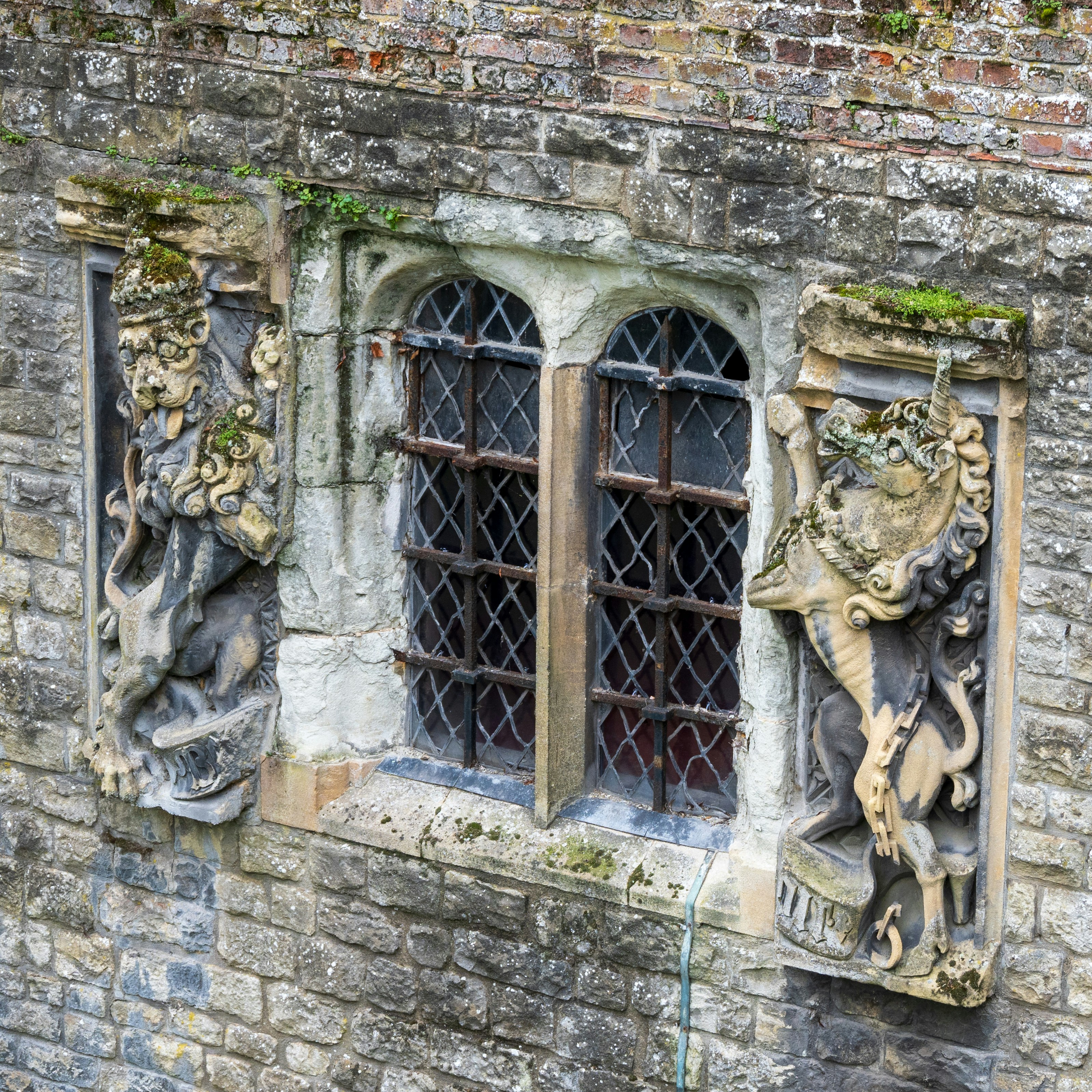 Intricate stone carvings of a lion and a mythical creature flanking a historic window, showcasing detailed craftsmanship and mossy textures.