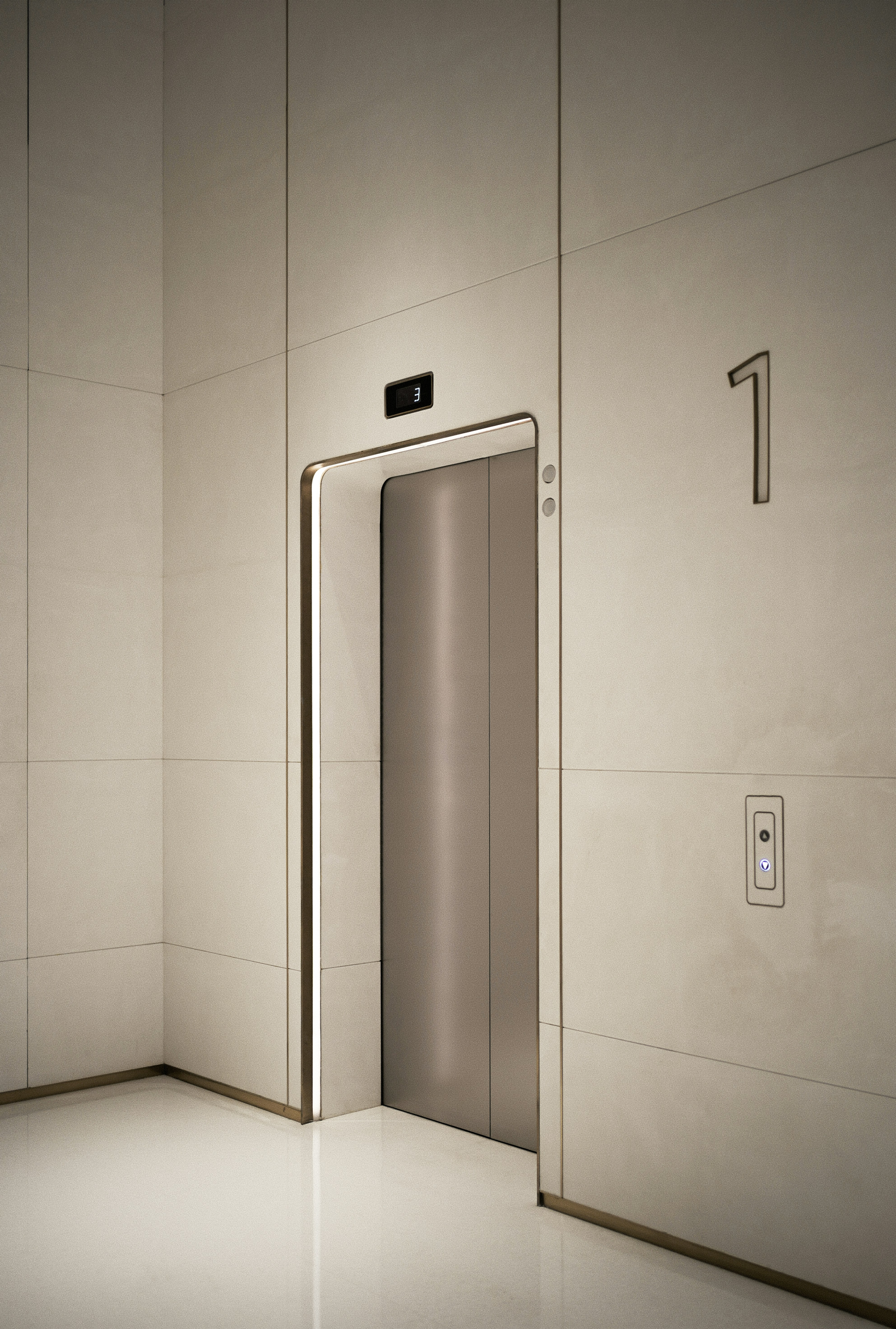 An elevator entrance in a high-end shopping mall. I'm a telephoto enthusiast and rarely use 35mm lenses in general because I find wide angle lenses to be poorly composed most of the time and have a stronger perspective that needs to be corrected when photographing architecture. | a white room with a silver door and a white wall
