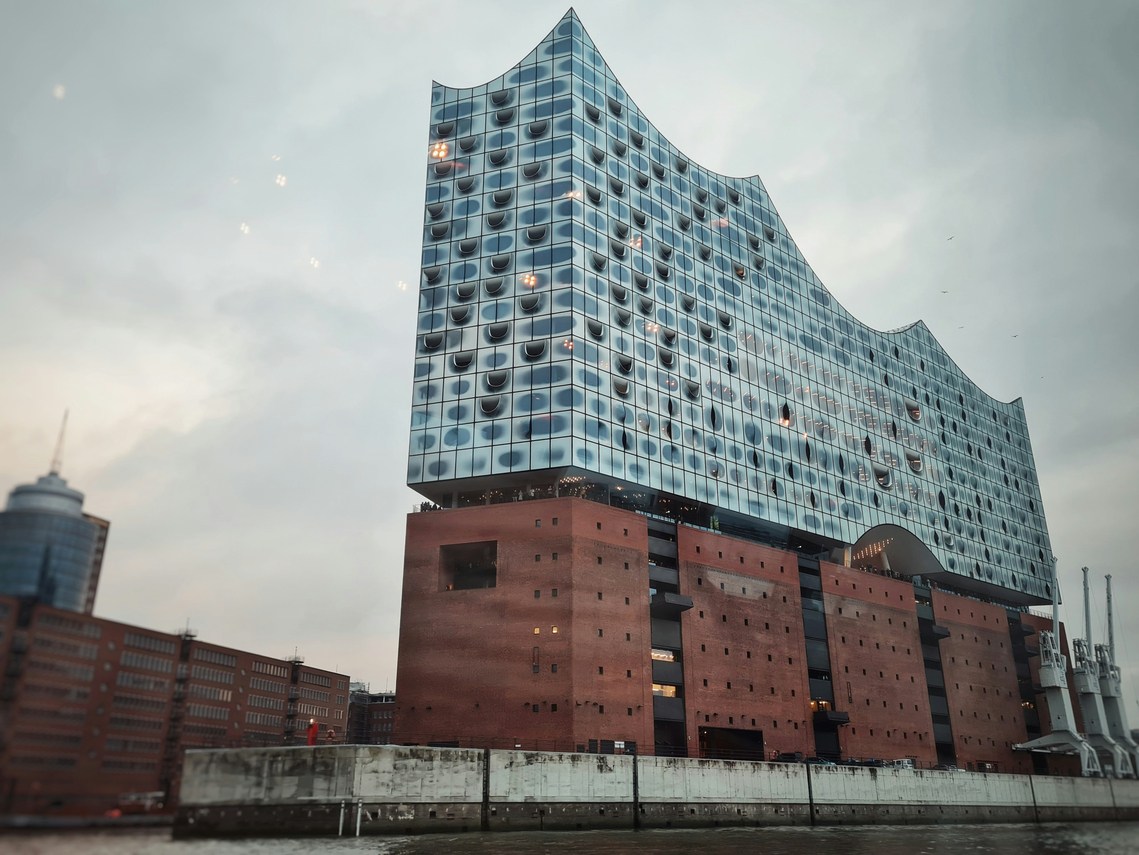 Harpa Concert Hall's glass-waves facade dominates the frame at dusk, perched above a brick harbor base.