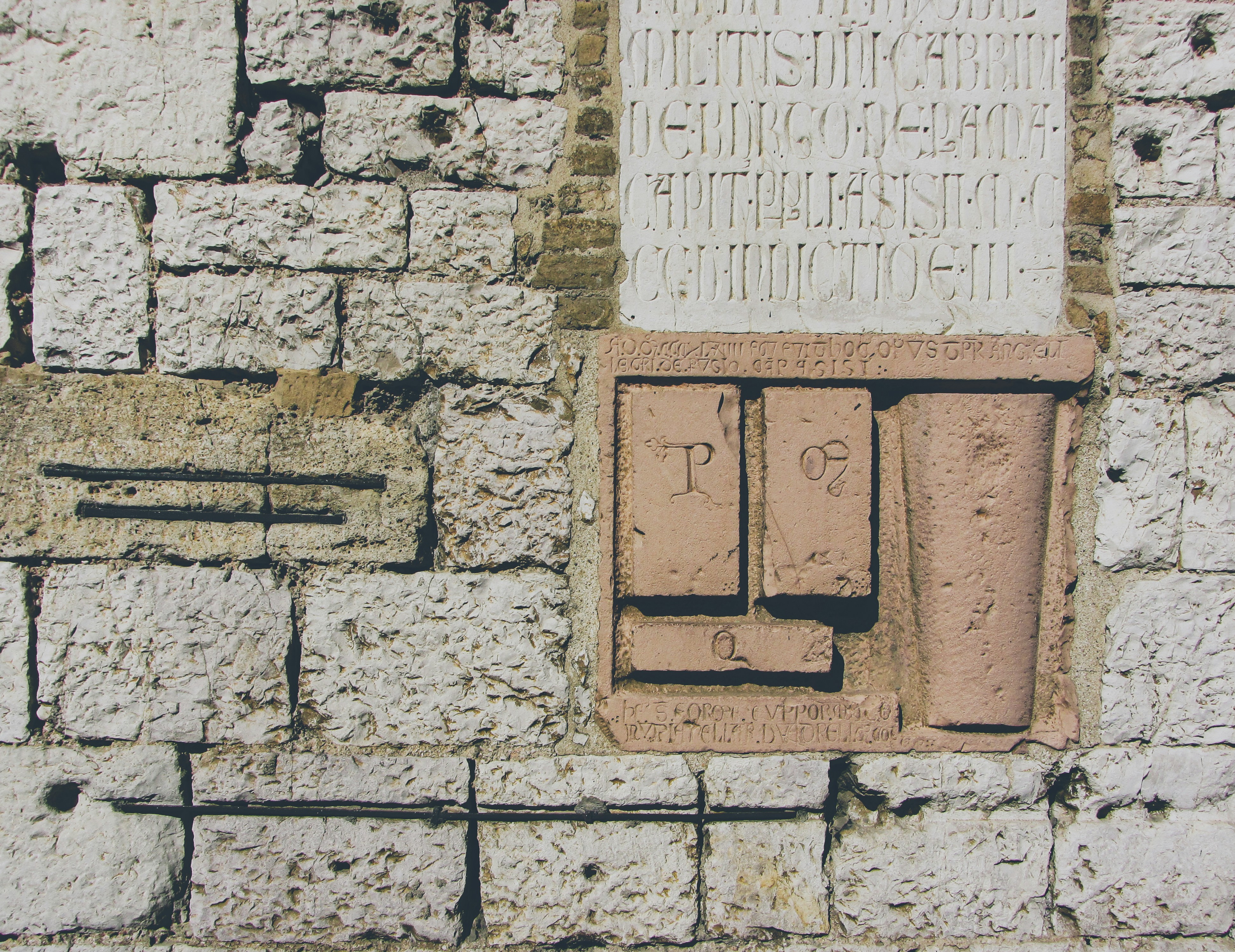 Weathered stone wall featuring mounted medieval measurement units and engraved text.