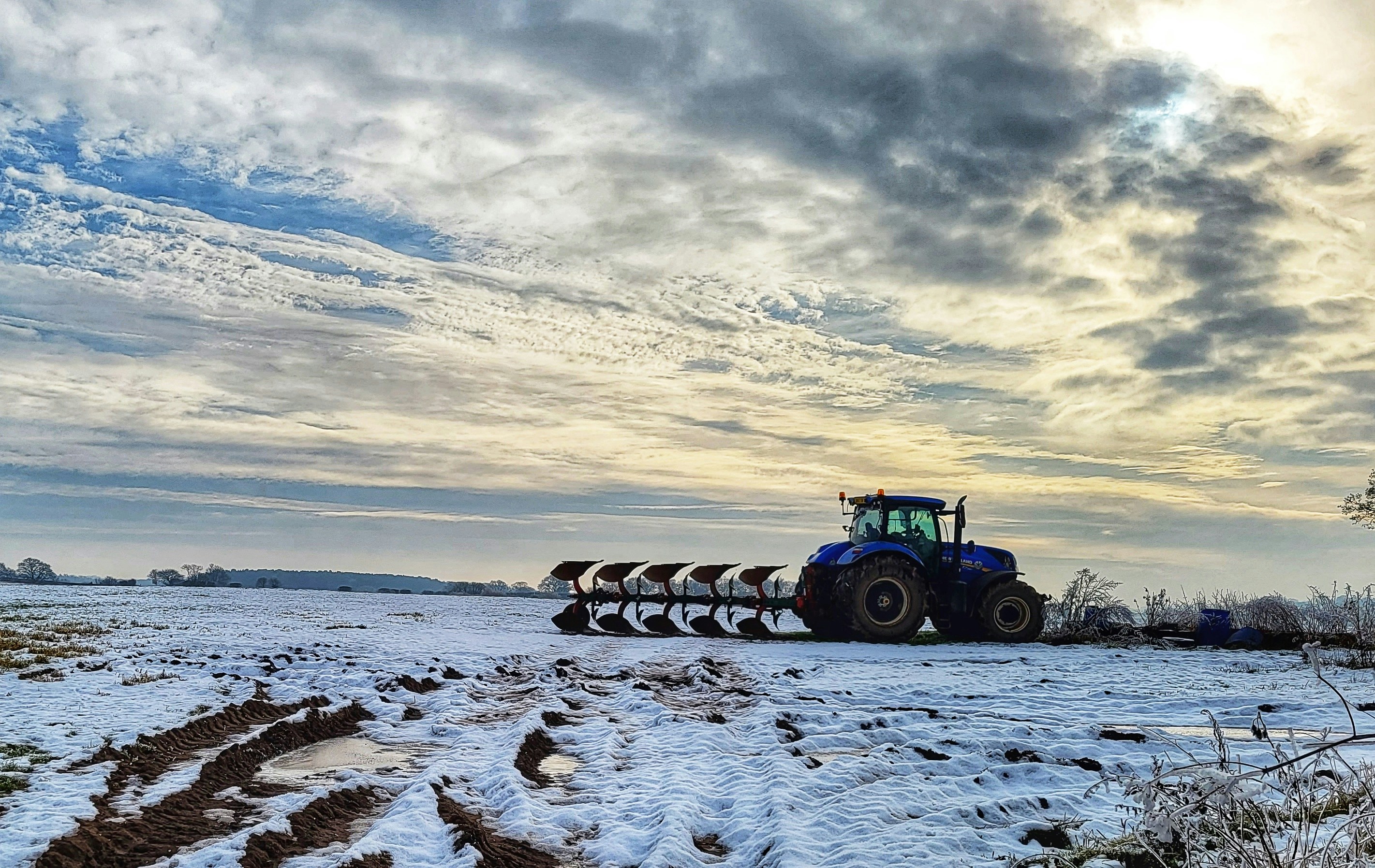 A tractor is pulling a plow through a snowy field photo – Free Sky ...