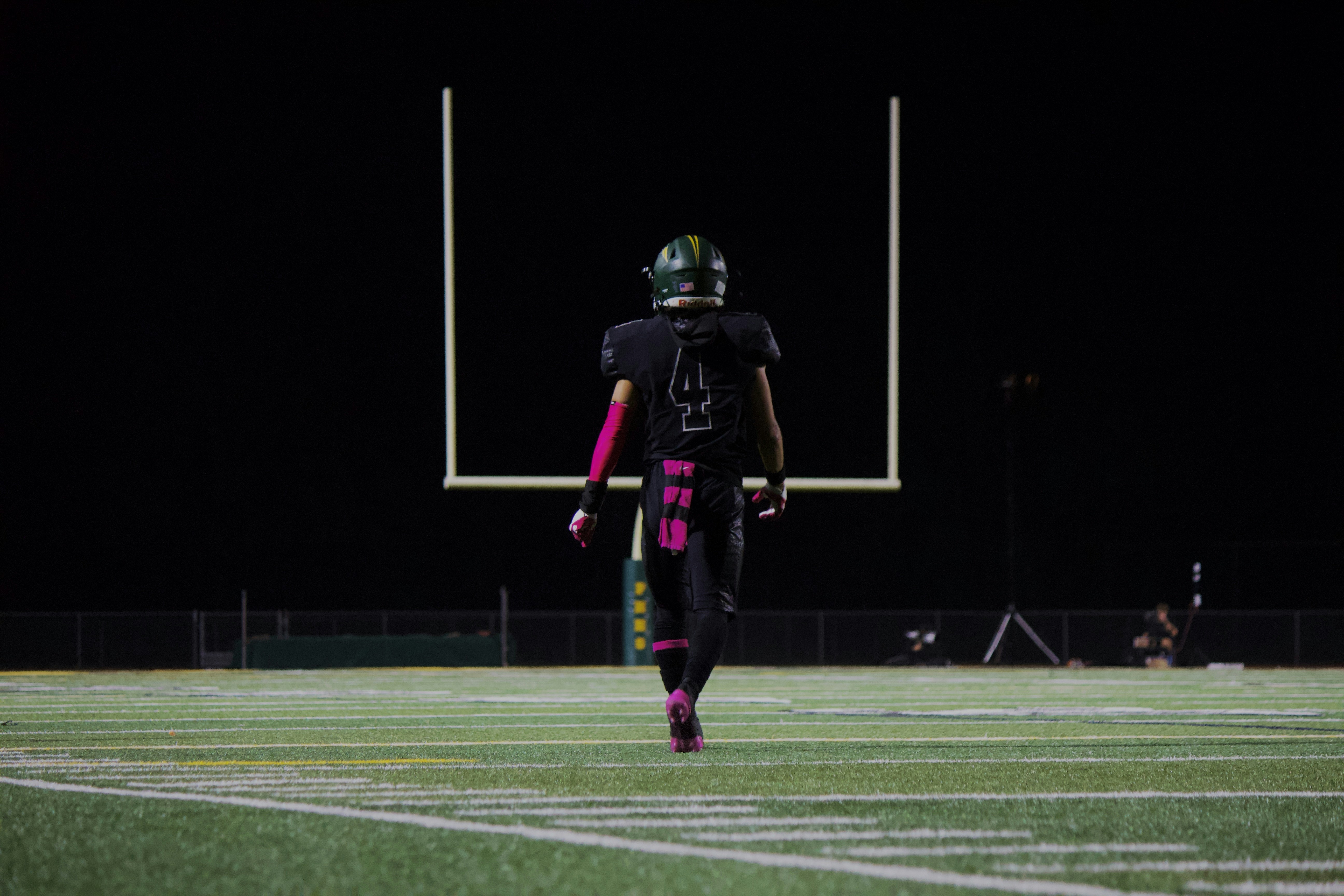 A football player walking across a field at night photo – Free Man ...