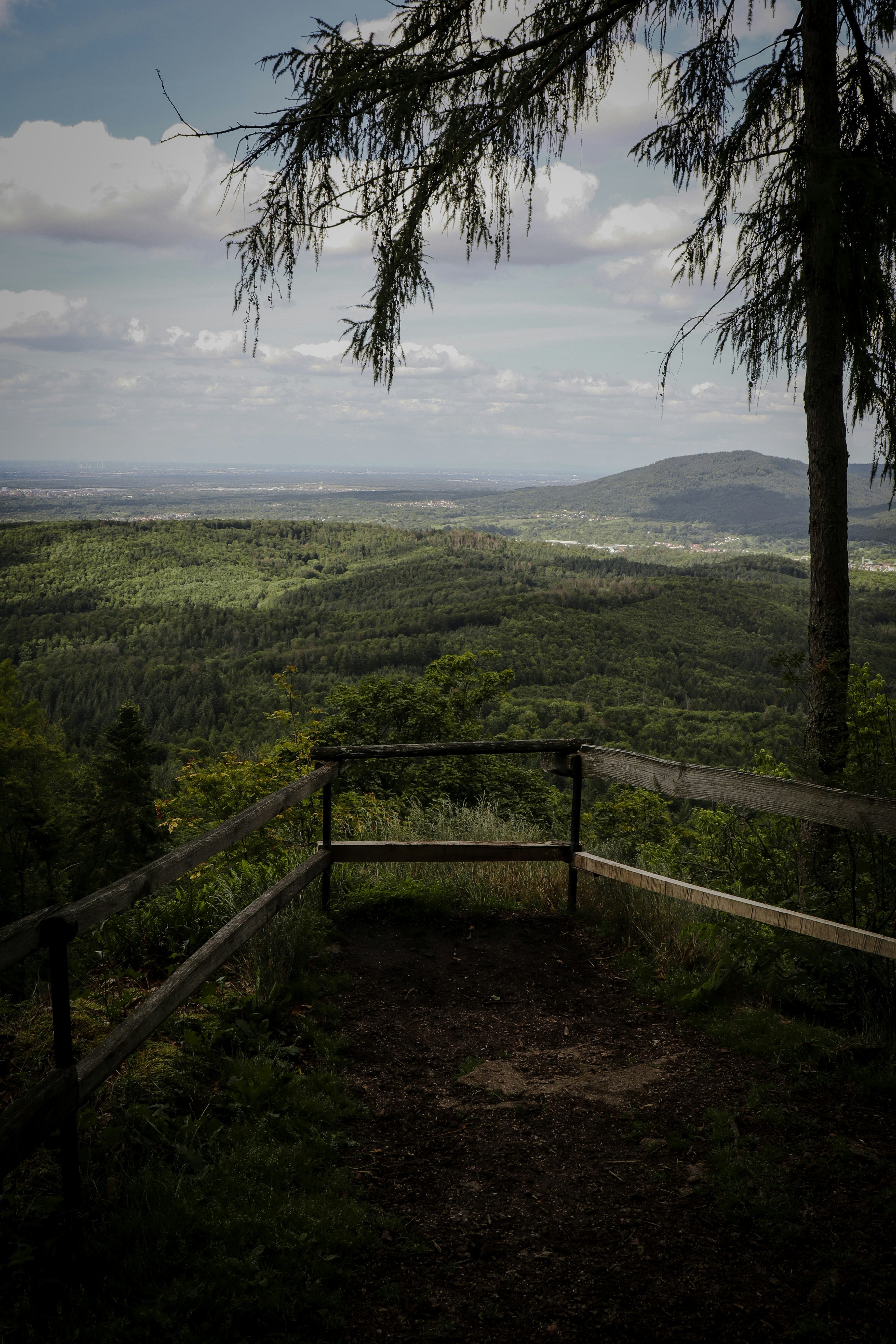 Ridge overlook with a rustic wooden fence leading the eye toward a layered valley and distant hills under a partly cloudy sky.