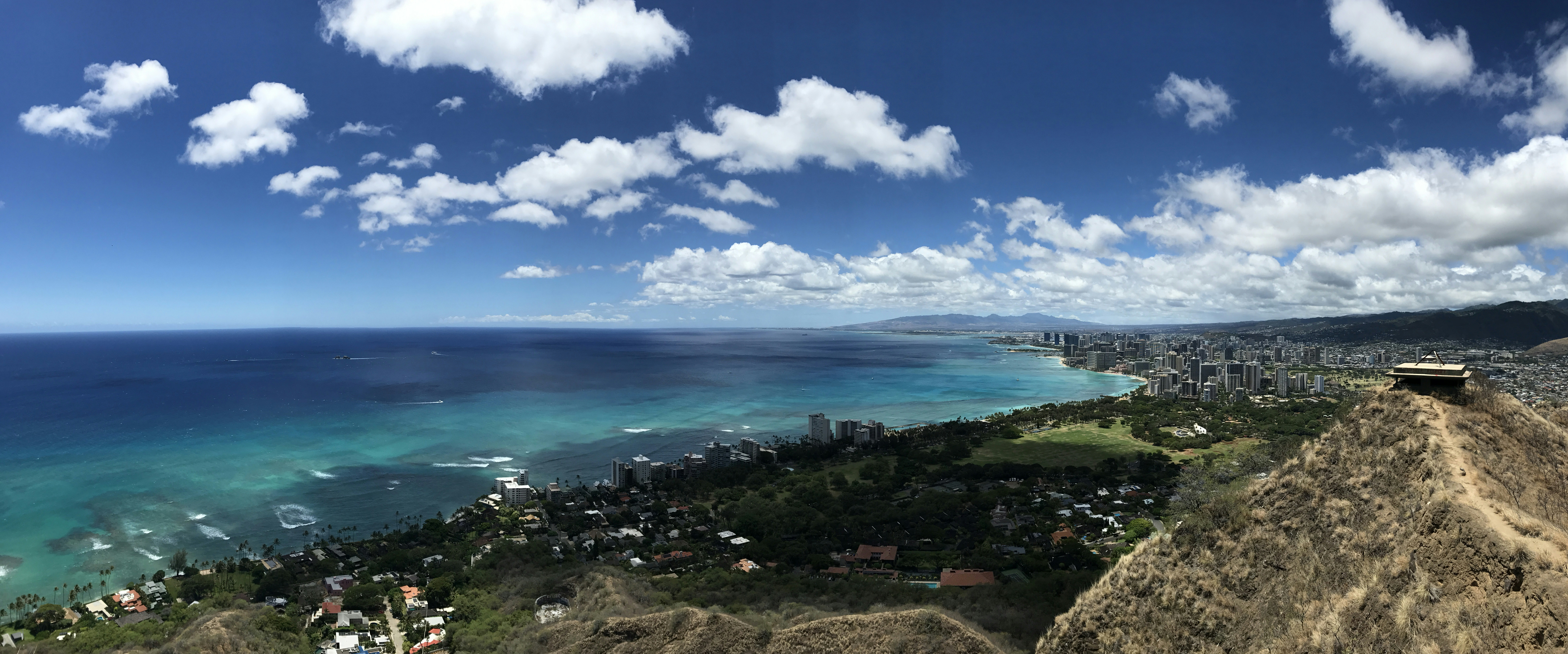 Panoramic view of a coastline with vibrant blue ocean and scattered clouds under a bright sky.