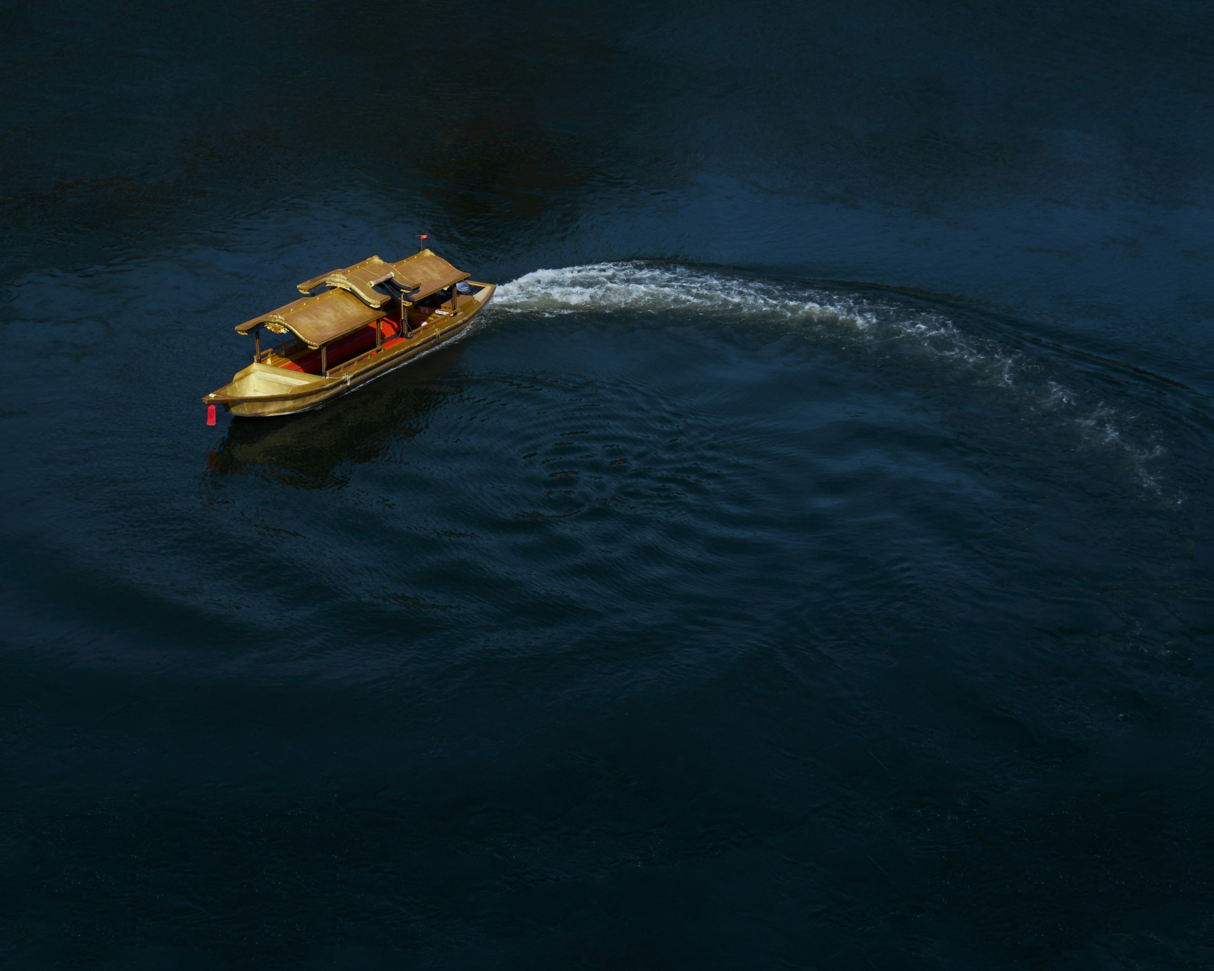 Crescent Wake: A tan-roofed boat glides through velvet blue waters