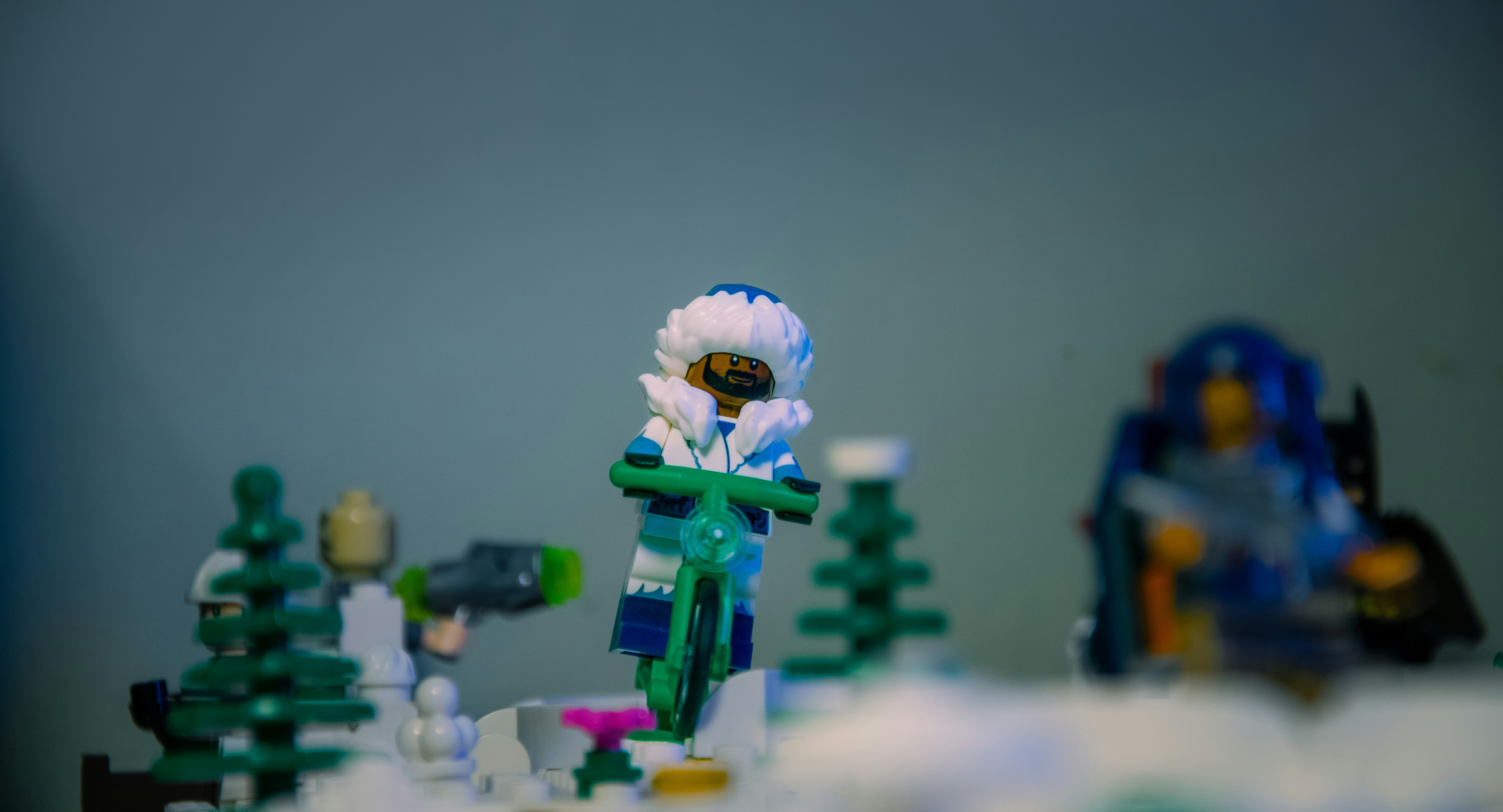 Miniature Winter Dash: LEGO Rider on a Green Scooter Through Snow and Pines