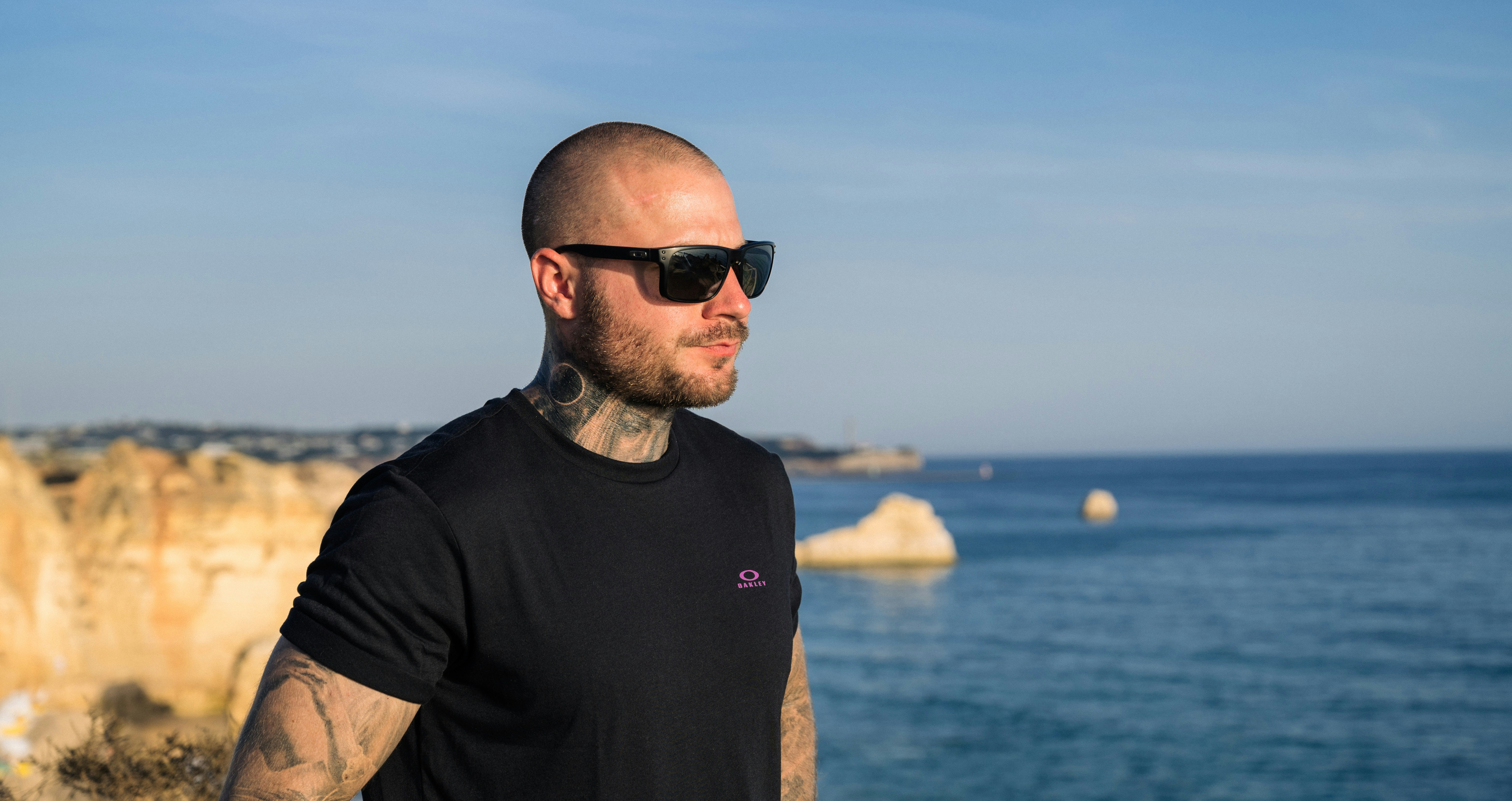 Cliffside Gaze: A Tattooed Portrait by the Azure Sea