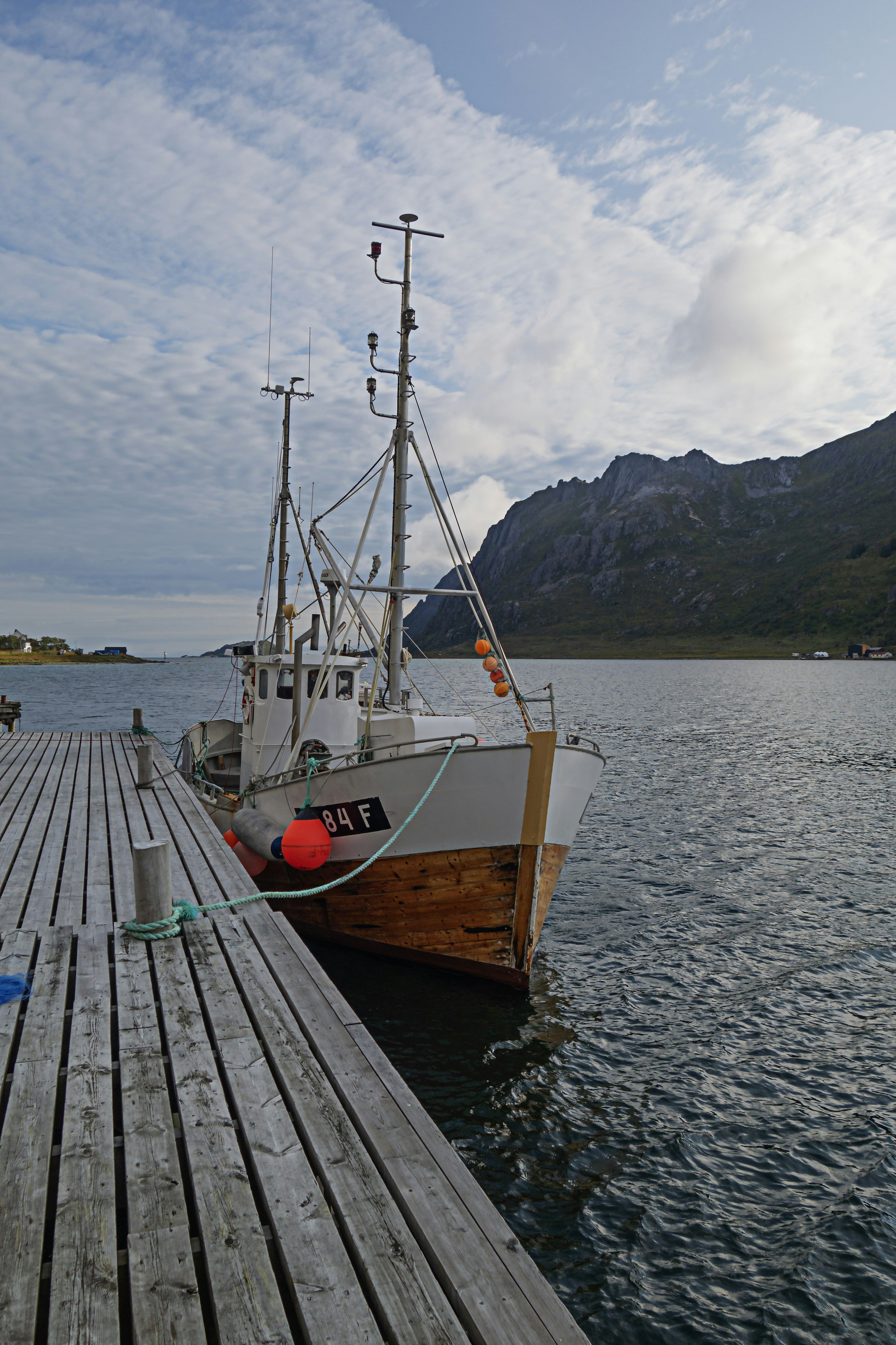 Harborbound: Weathered Fishing Boat Moored Along a Timber Pier Against Rugged Mountains