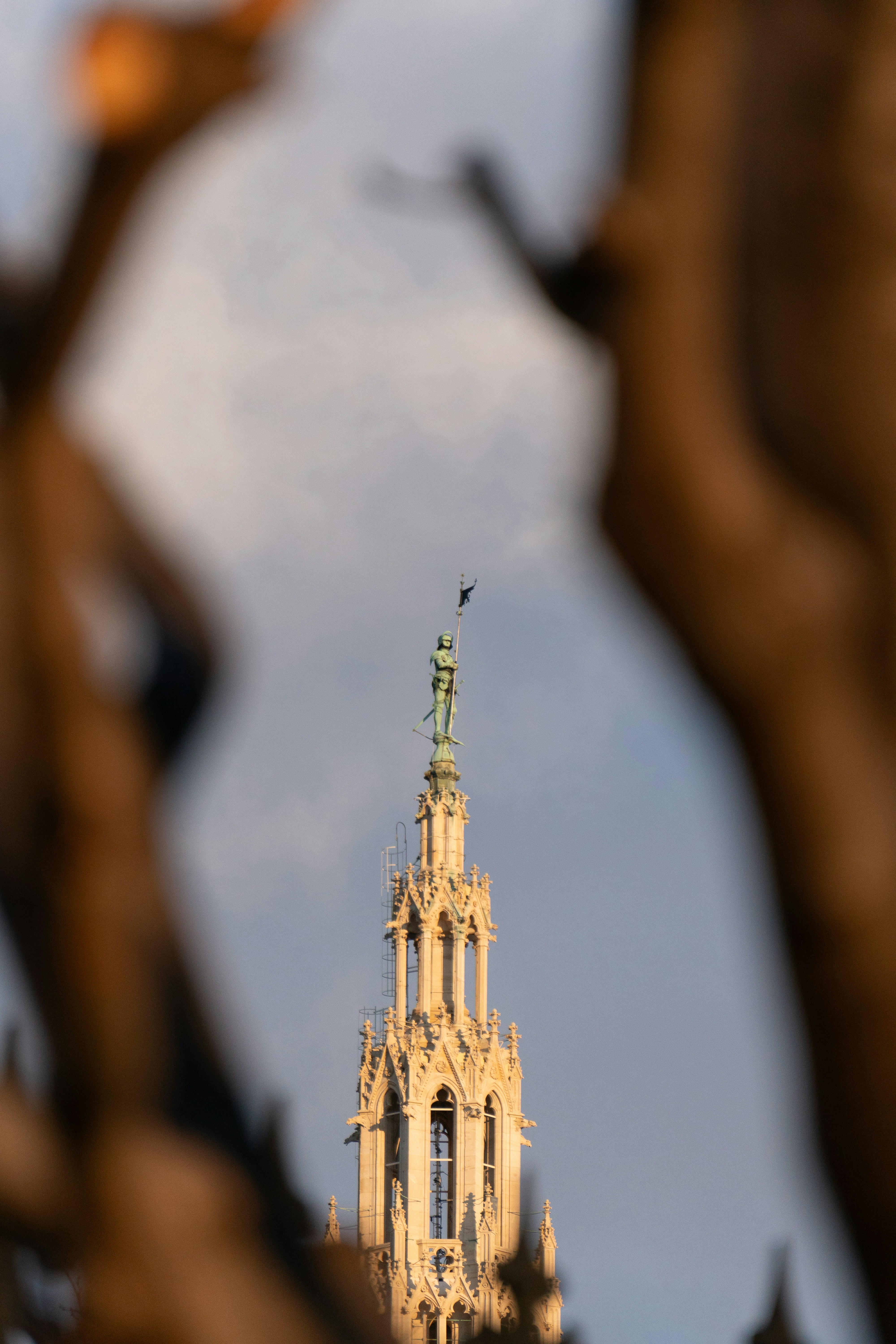 Framed Summit: a statue-topped Gothic spire rising through carved foreground arches