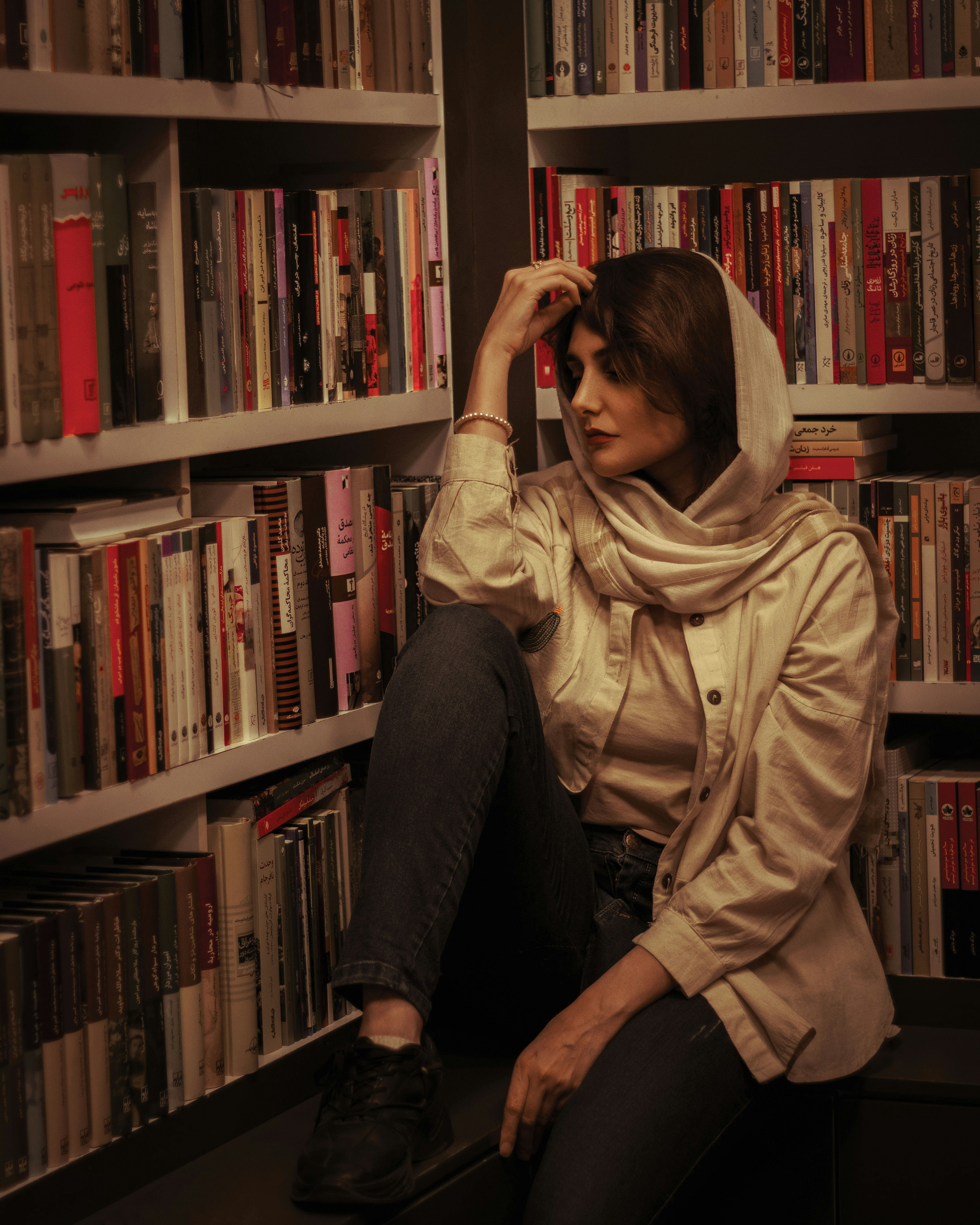 A woman sitting on a bench in front of a bookshelf photo – Free ...
